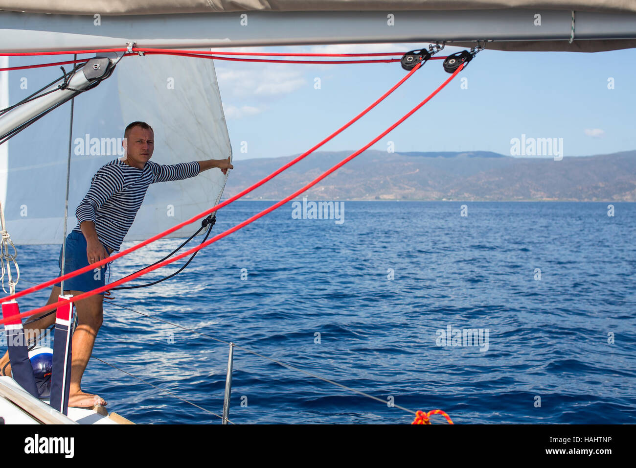 Young man near the sails on the boat. Setting the equipment on a ...