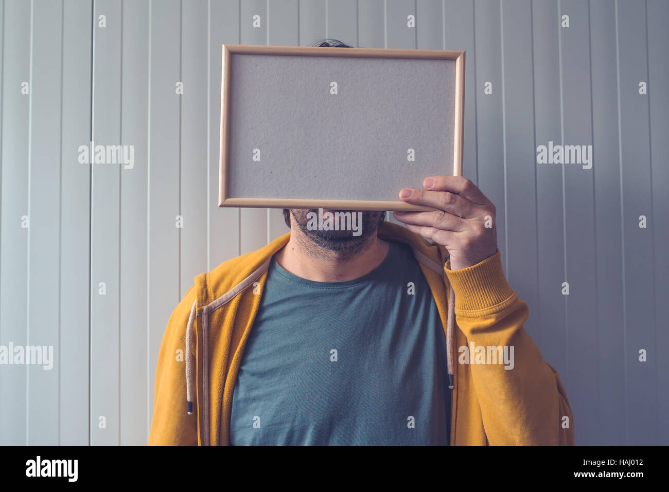 Unrecognizable man posing with blank picture frame over his face as ...