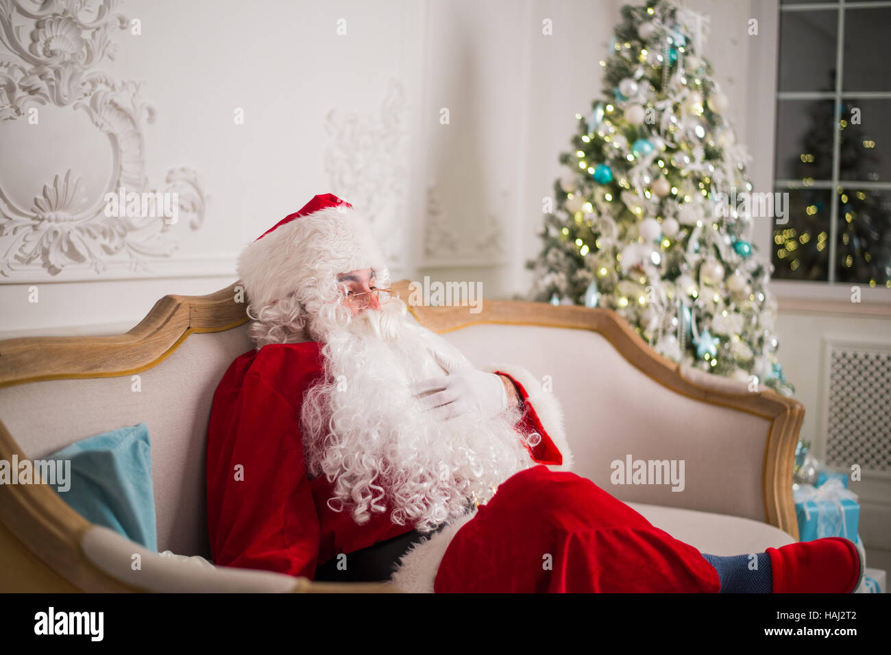 Santa Claus relaxing on sofa against christmas tree at home Stock Photo ...