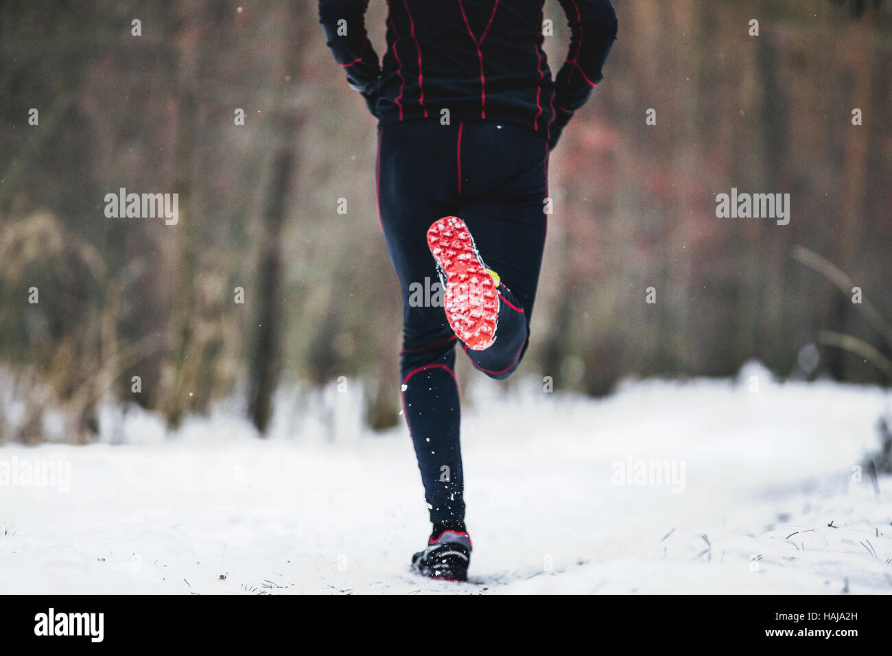 rear view athlete runner is running on a snowy trail in woods winter ...