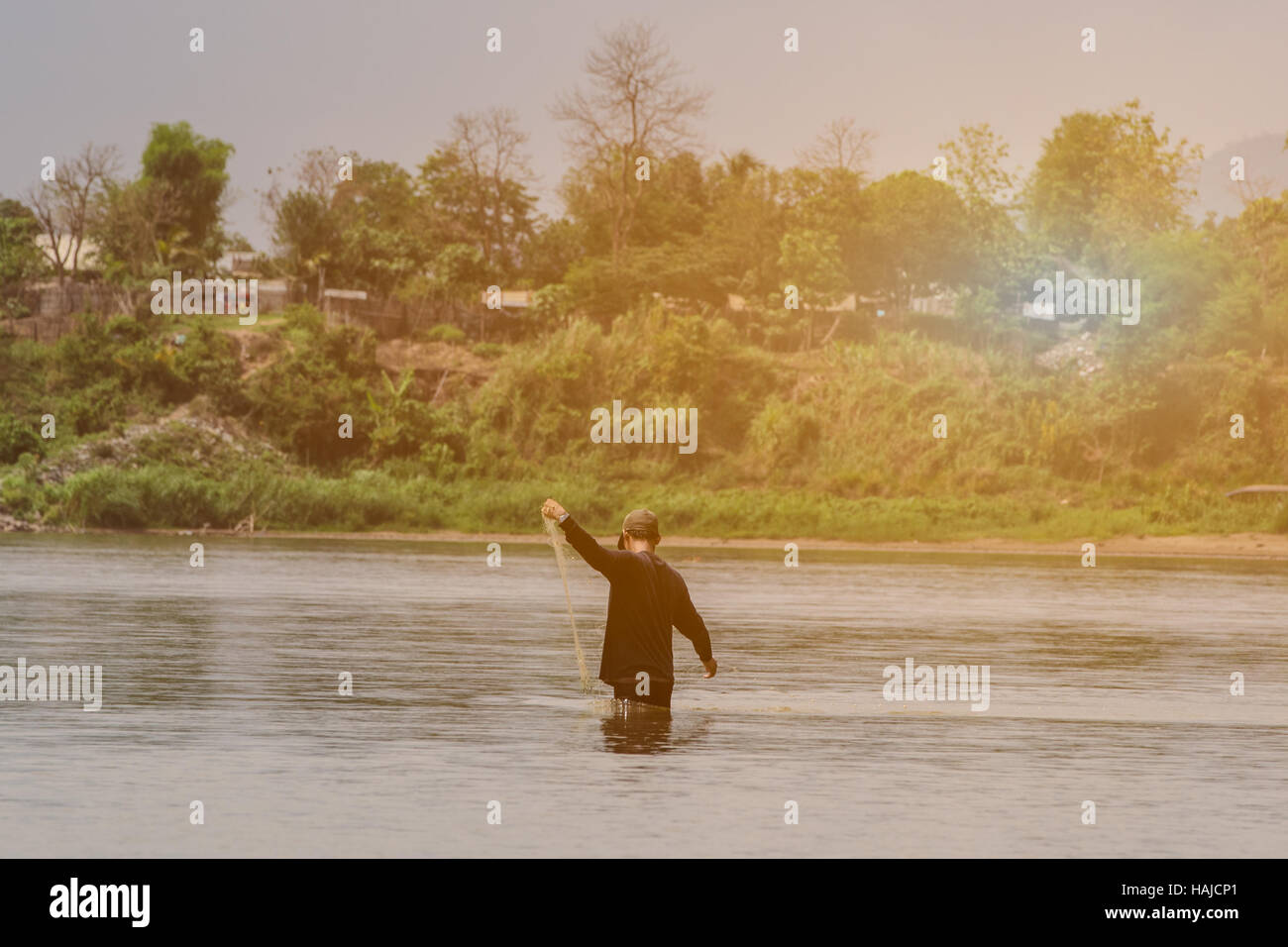 Back view of Asian fisherman stand in river and throwing fish net to ...