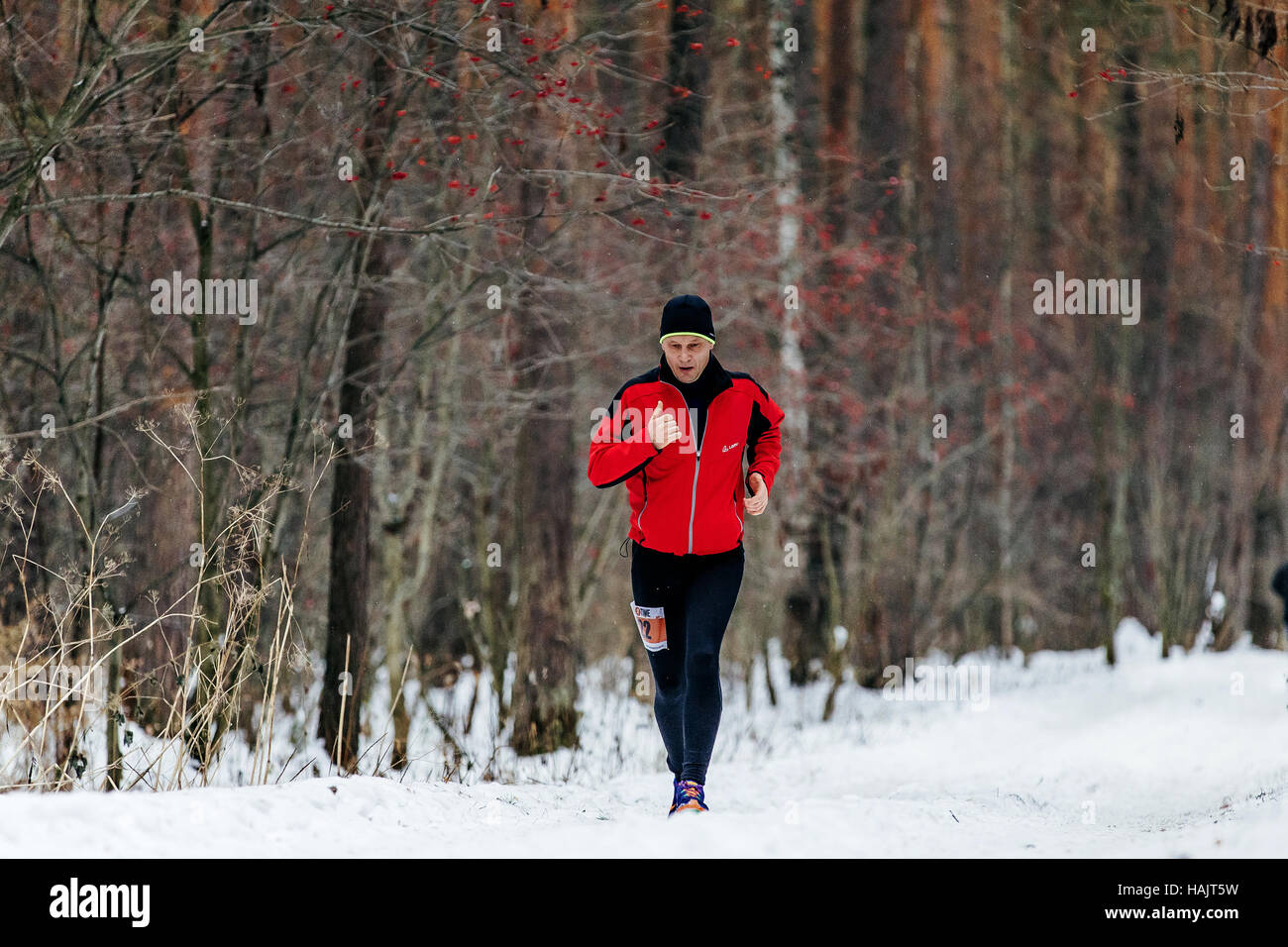 male runner running on a snowy trail in pine forest during Winter ...