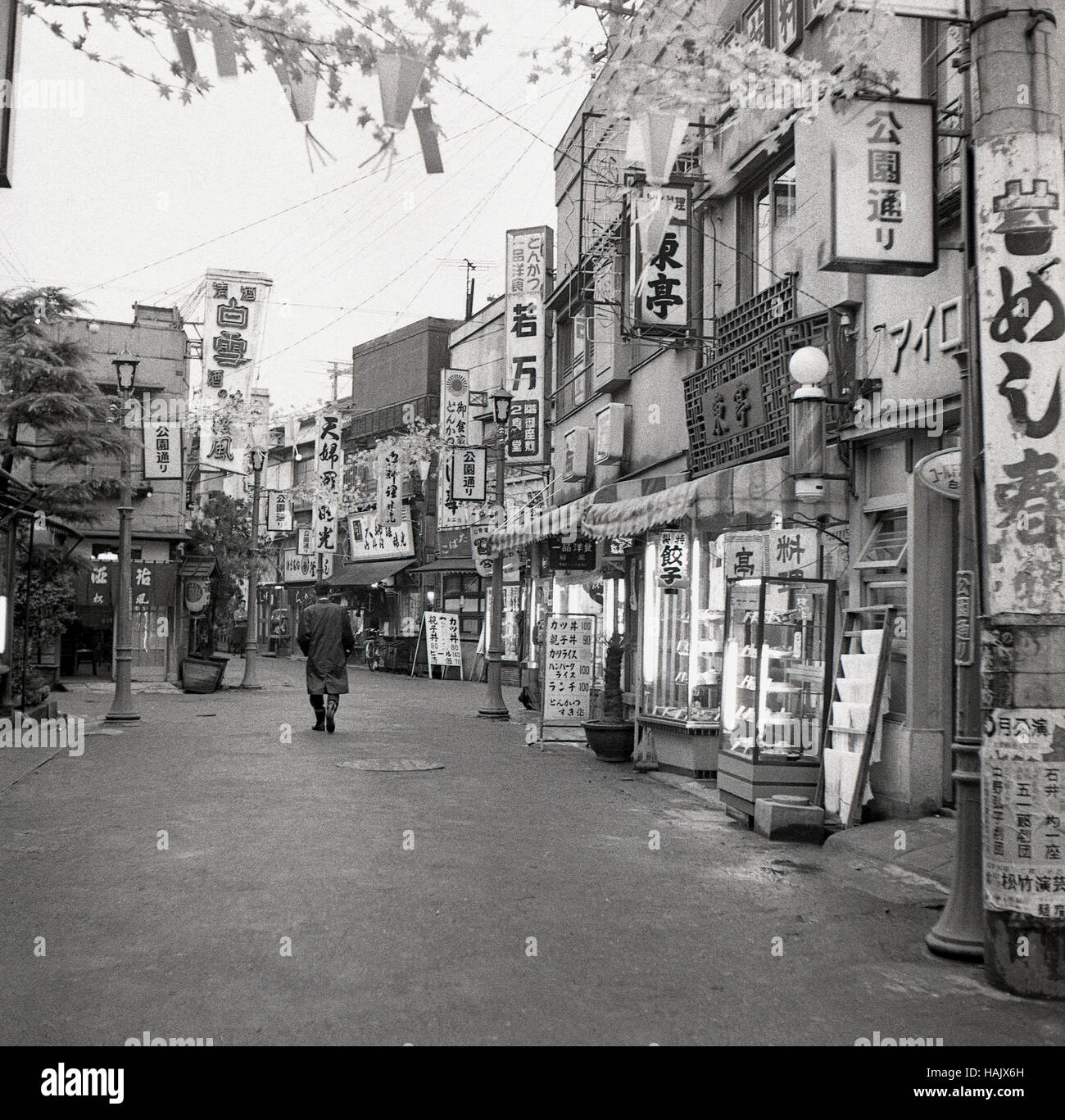 1950s, historical, a man walking down pass the retail stores and ...
