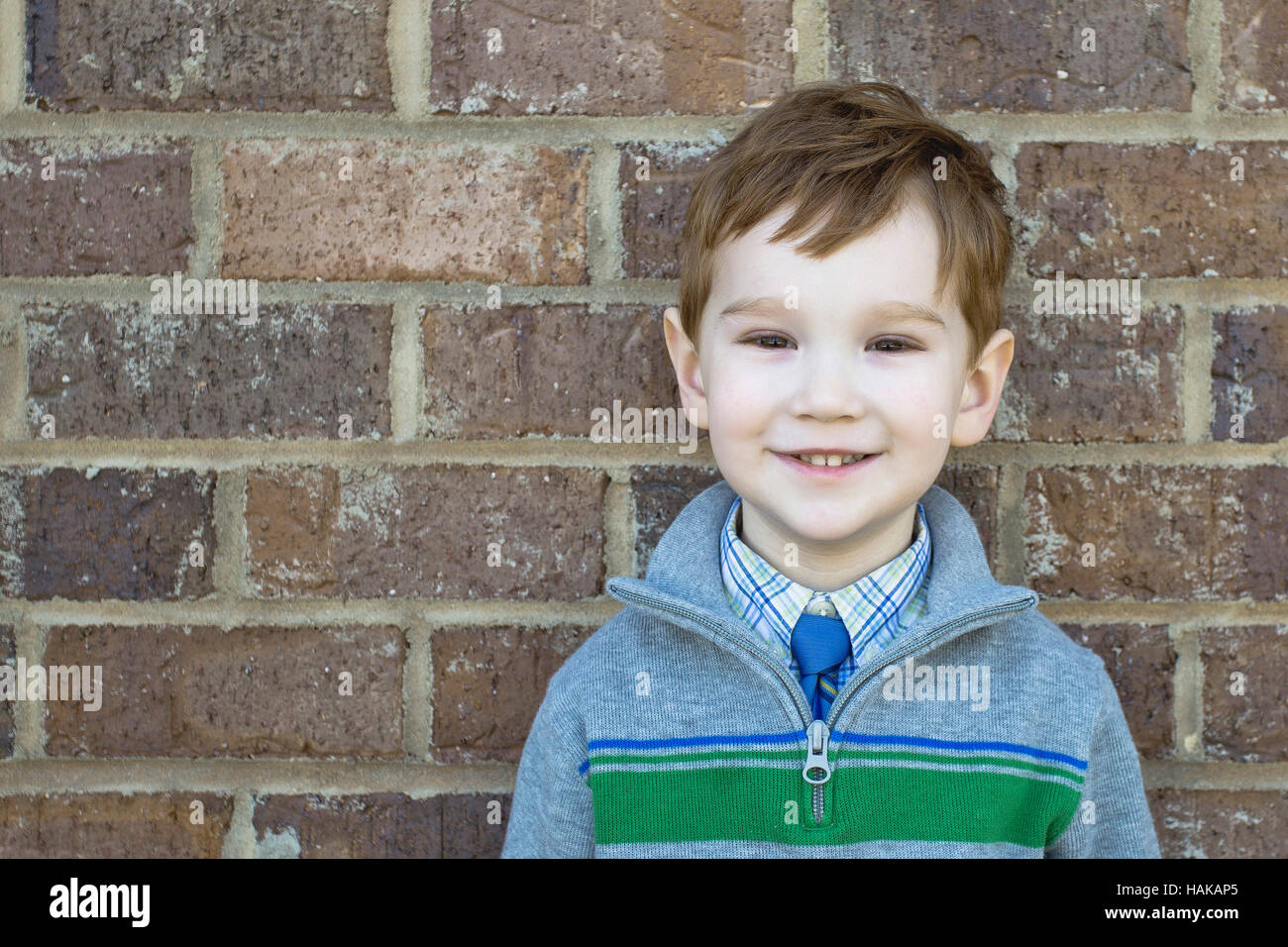 Smiling cute boy up against a brick wall Stock Photo - Alamy