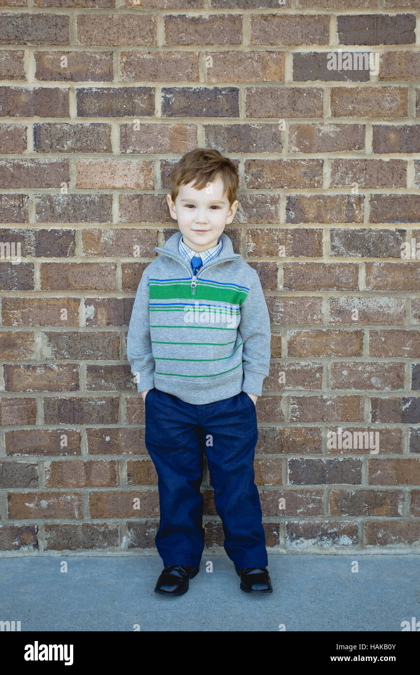 Smiling cute boy standing up against a brick wall Stock Photo - Alamy