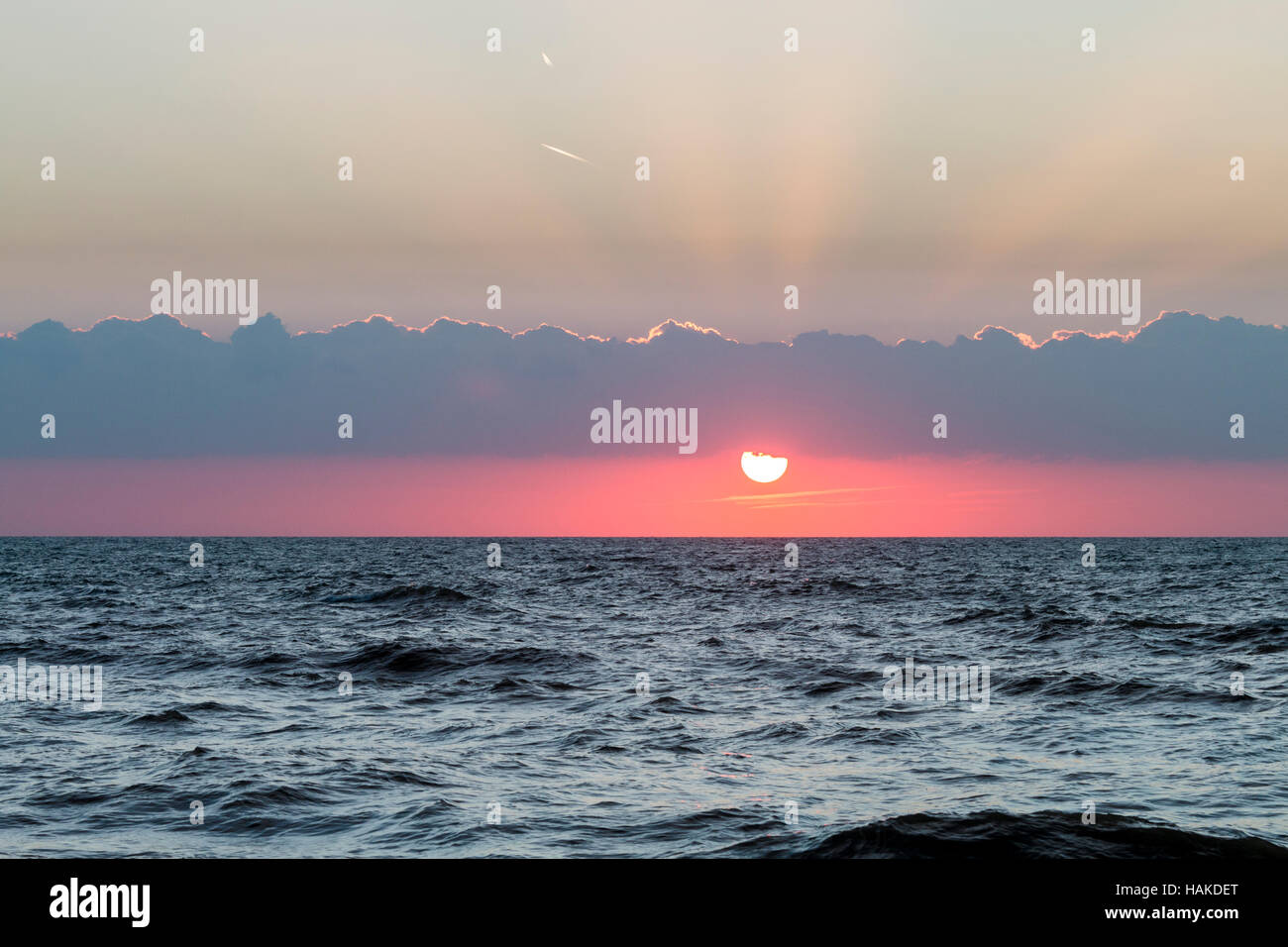 Sun just above horizon over the sea. Layer of red sky on horizon with ...