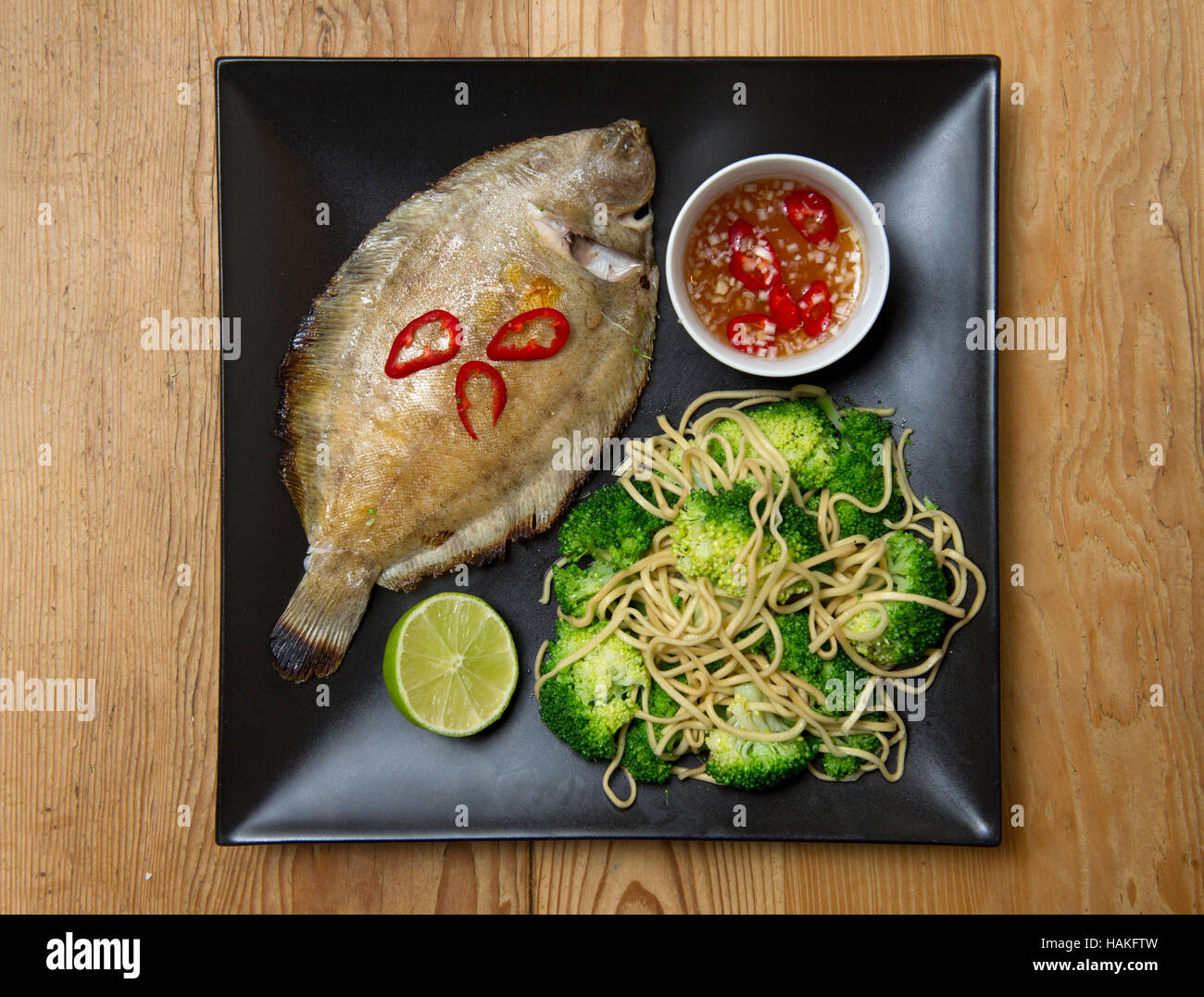 A plaice with Brussels sprouts and noodles on a square black dish Stock ...