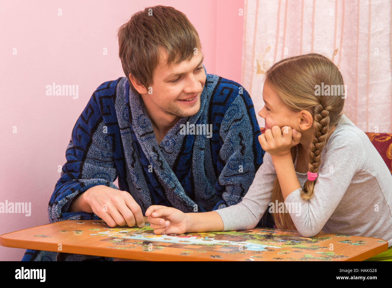 Father and daughter looked at each other collecting puzzle elements ...