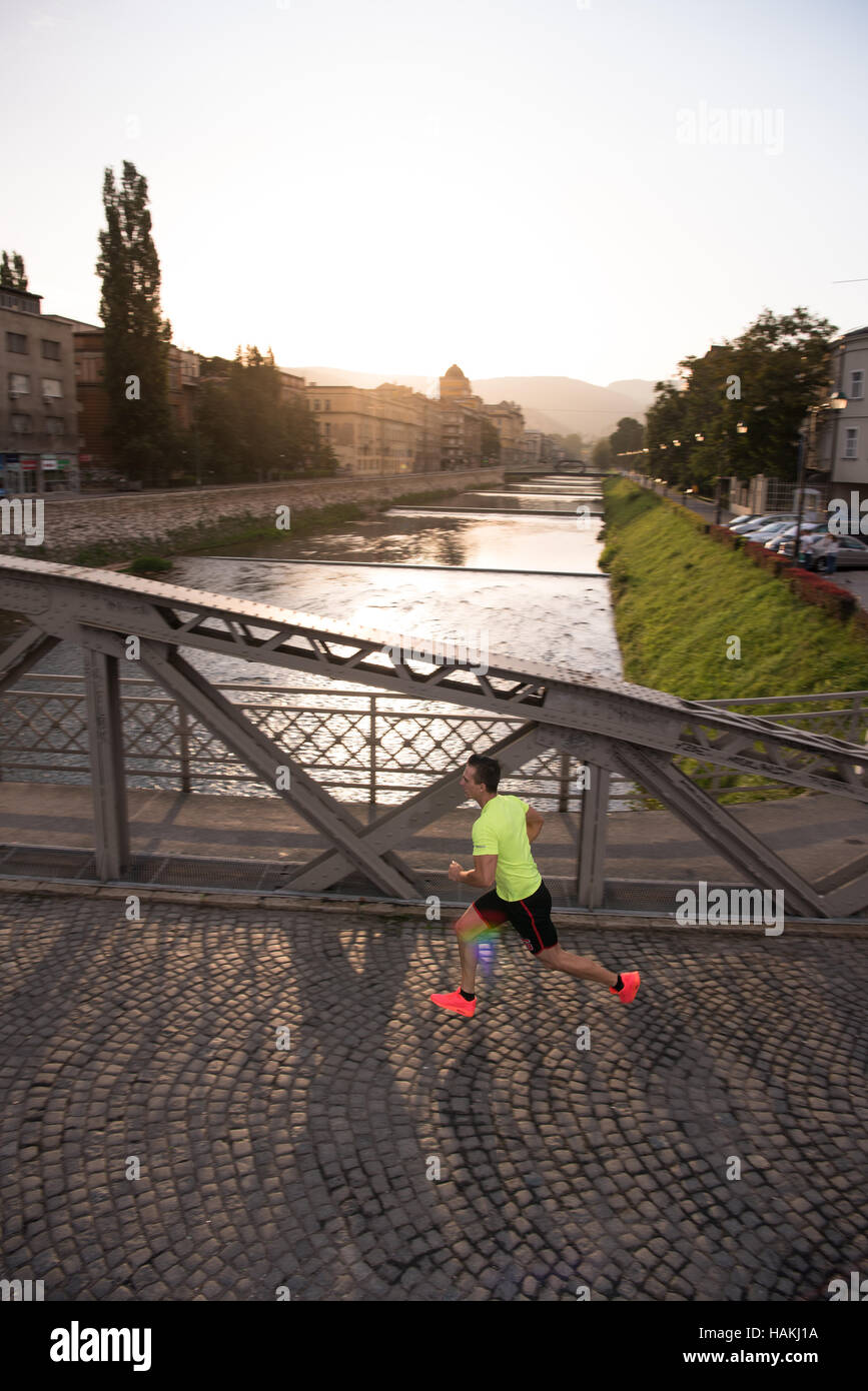 Young sporty man running on sidewalk at early morning jogging with city ...