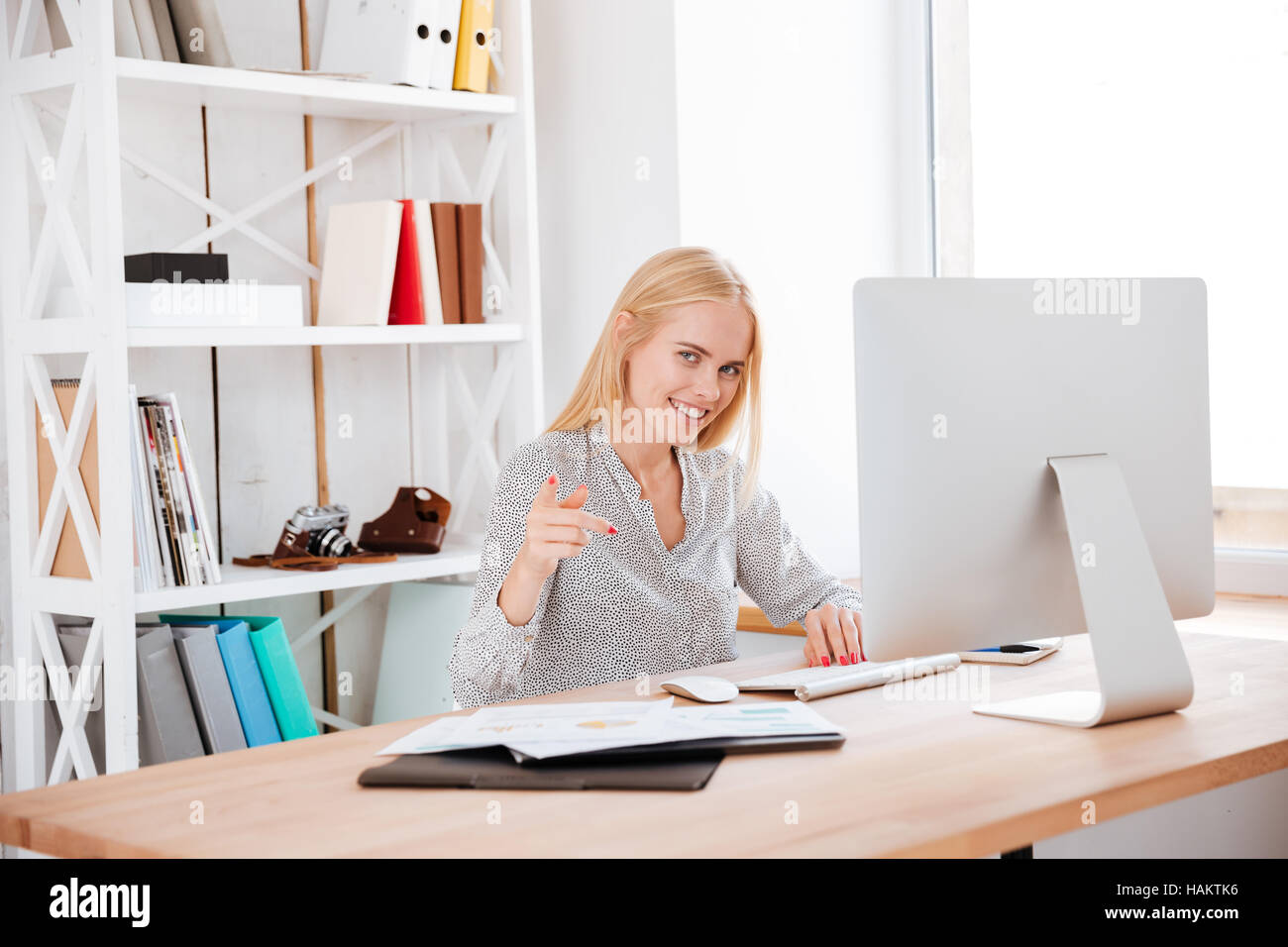 Smiling pretty business woman sitting at her workplace and pointing ...