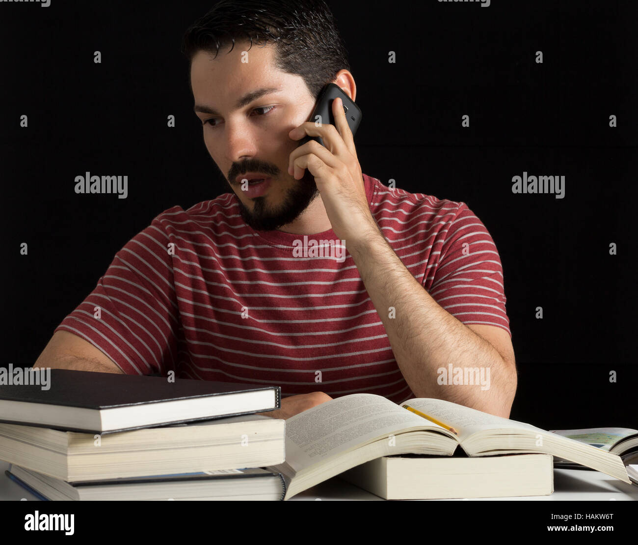 Young man with cellphone and books over table. Black background Stock ...
