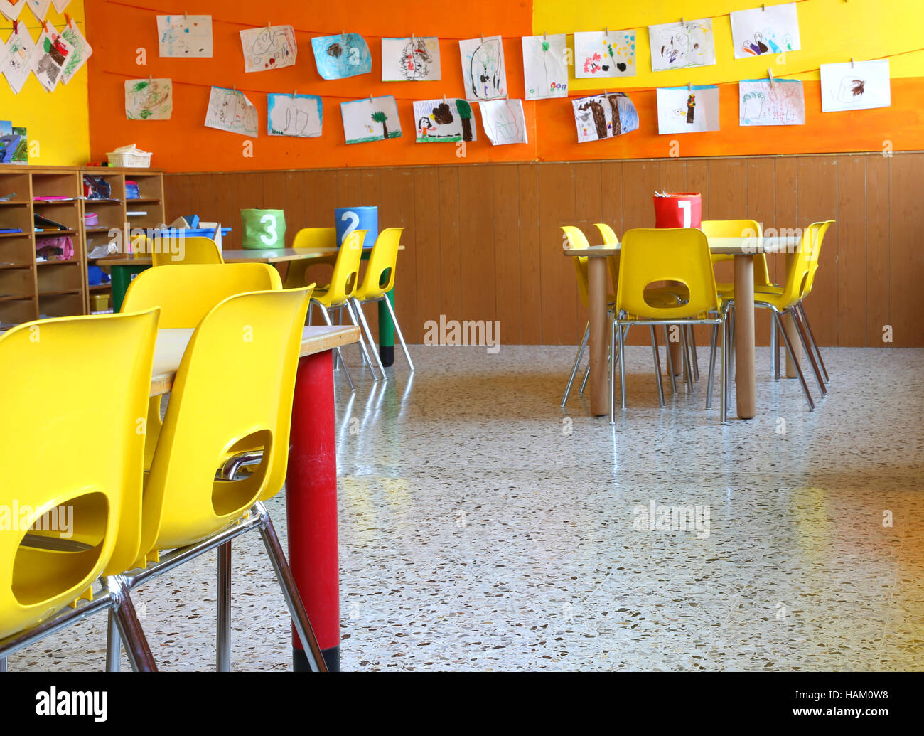 wide classroom of a nursery school with tables and chairs and drawings ...