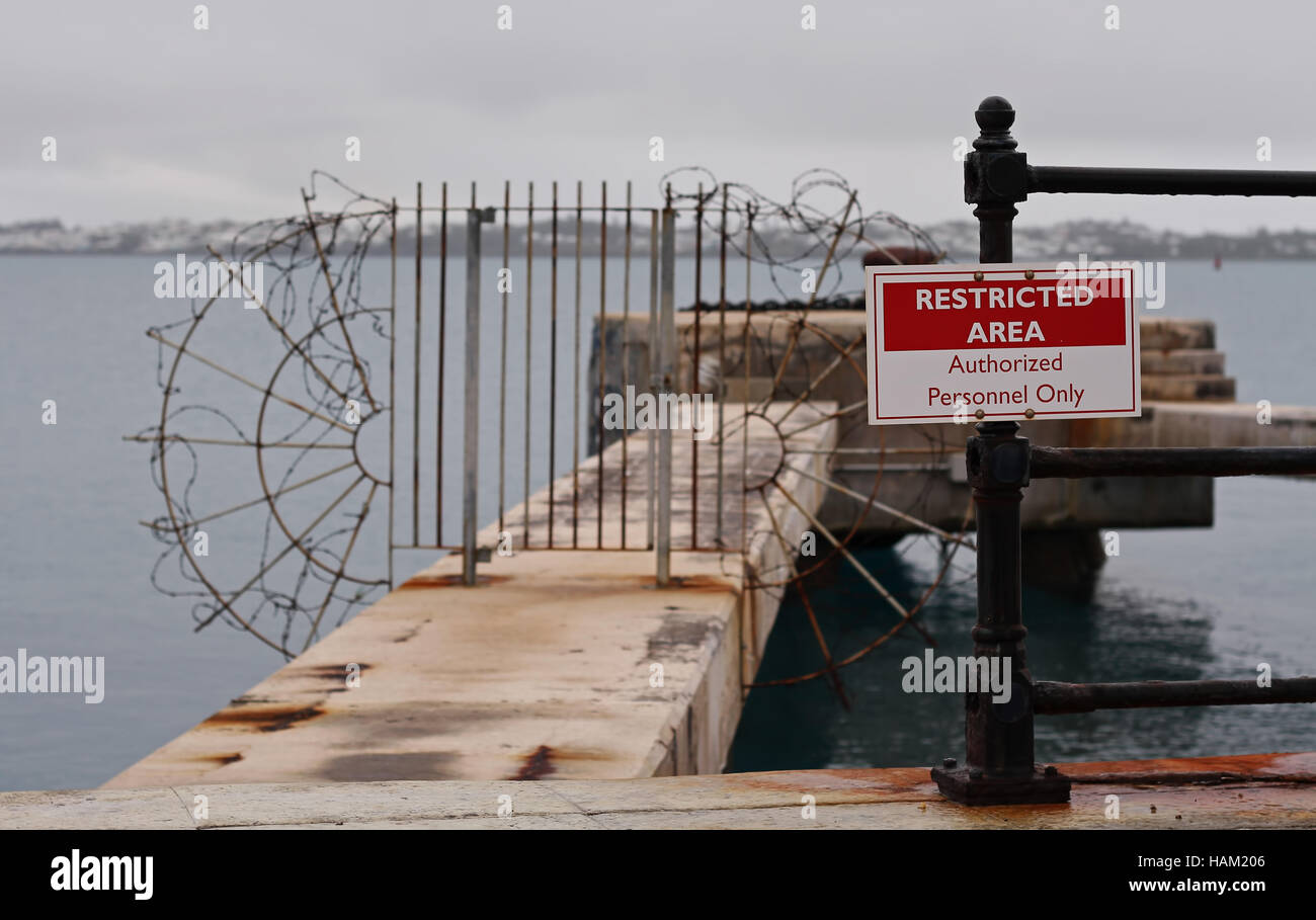 A restricted area sign, in front of a locked gate surrounded by barbed ...
