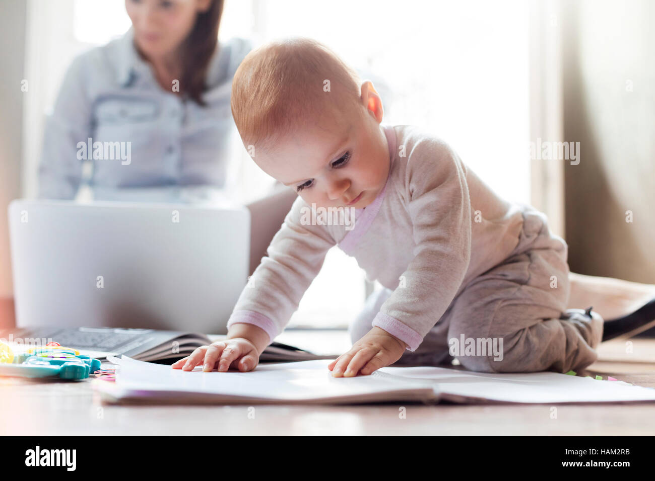 Baby girl playing on floor near mother working on laptop Stock Photo ...