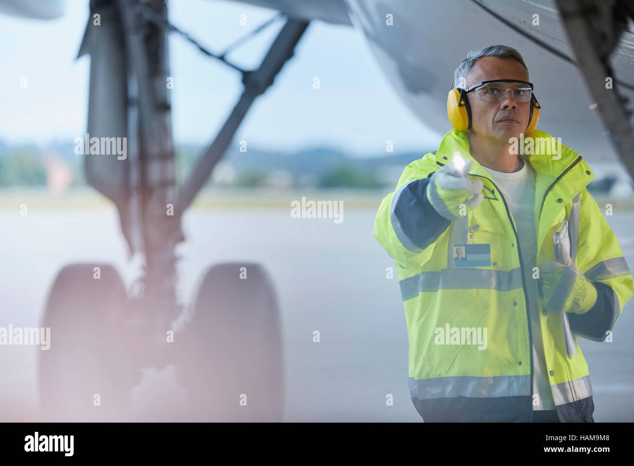 Air traffic controller with flashlight under airplane on airport tarmac ...