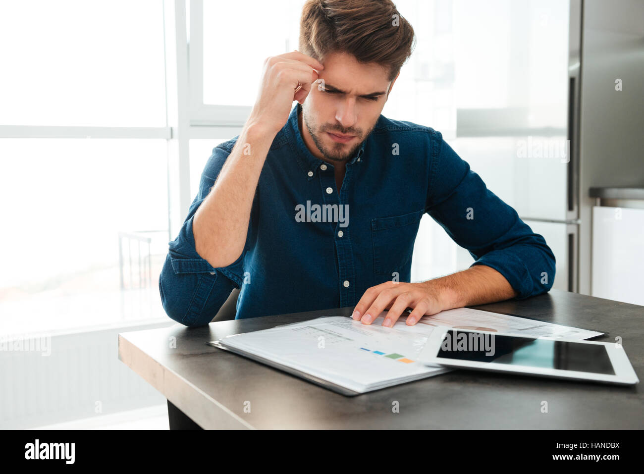 Photography of concentrated young man sitting at home and analyzing his ...