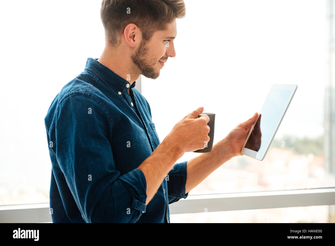 Picture of young cheerful man holding tablet and drinking coffee near ...