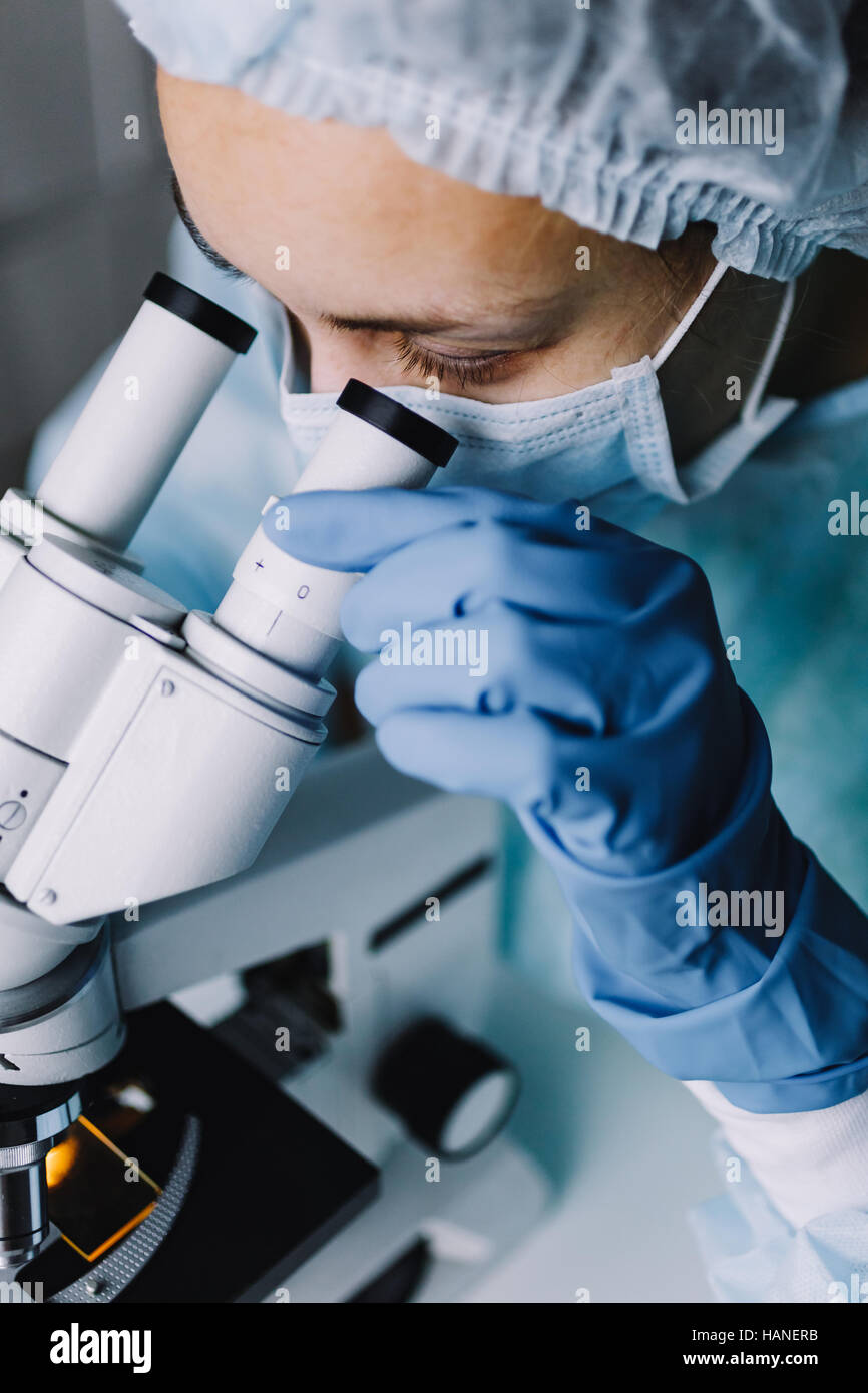 Young scientist in uniform looking at microscope Stock Photo - Alamy