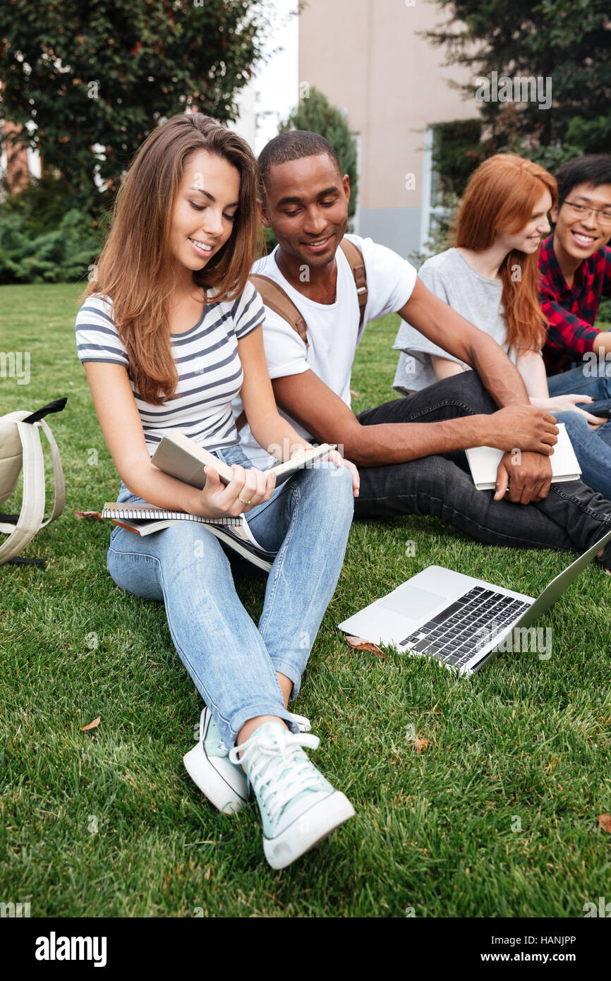 Multiethnic group of happy young people reading book and using laptop ...