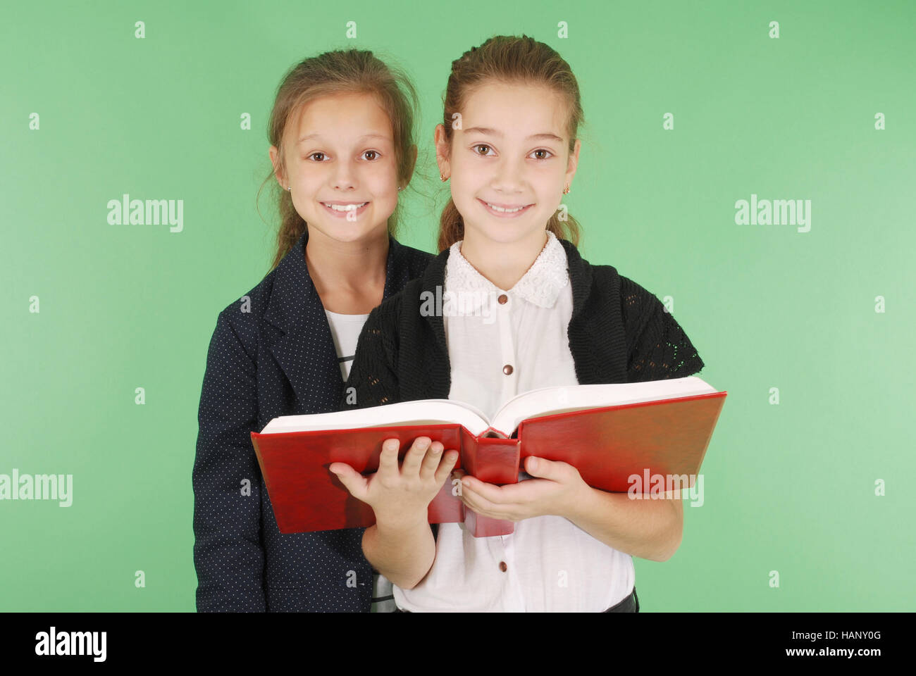 Two young school girls with red book isolated on green Stock Photo - Alamy