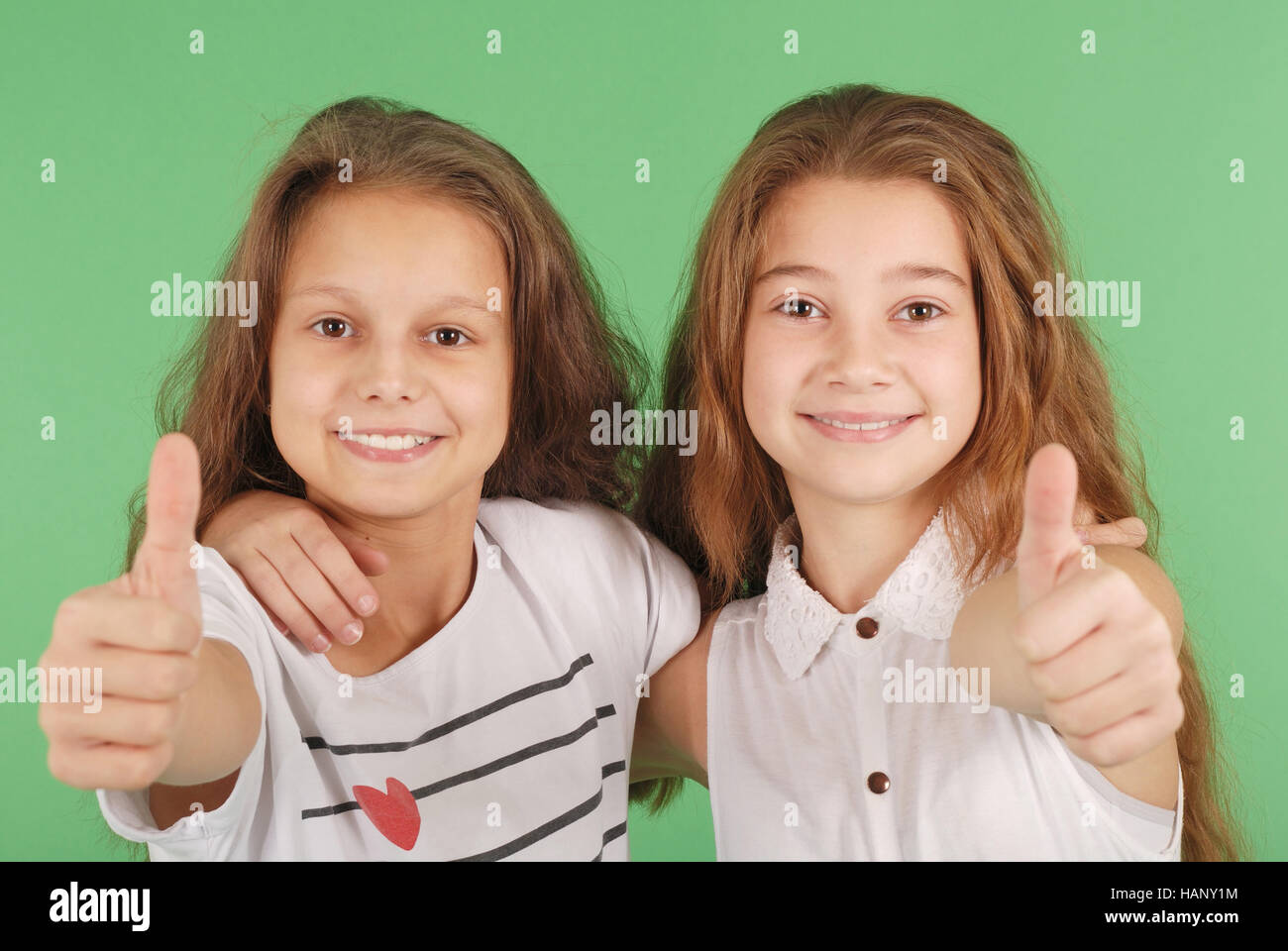 Two smiling young school girls showing thumbs up isolated on green ...