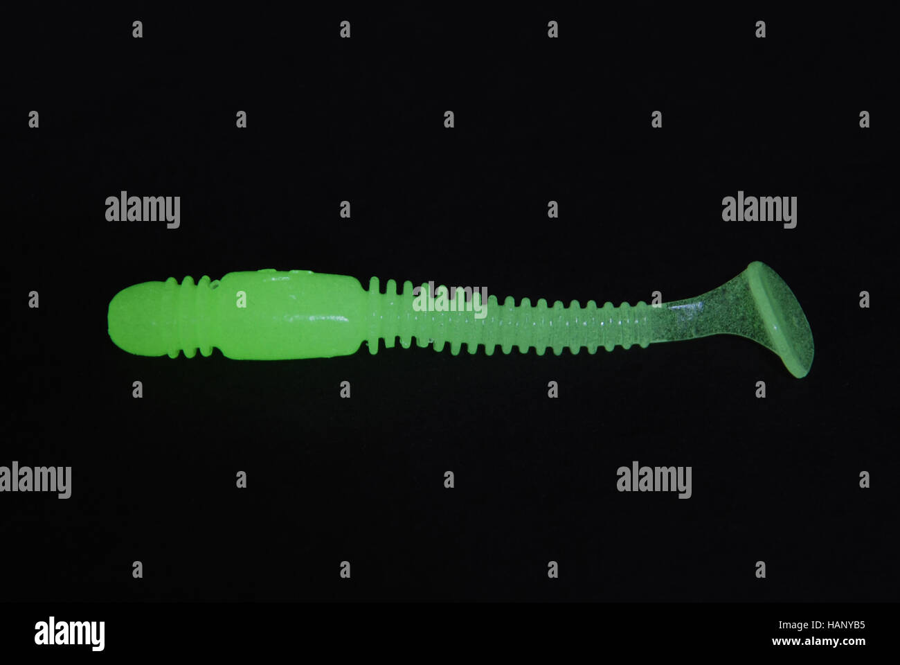 One green bait fishing fluorescent twister isolated on black backround ...