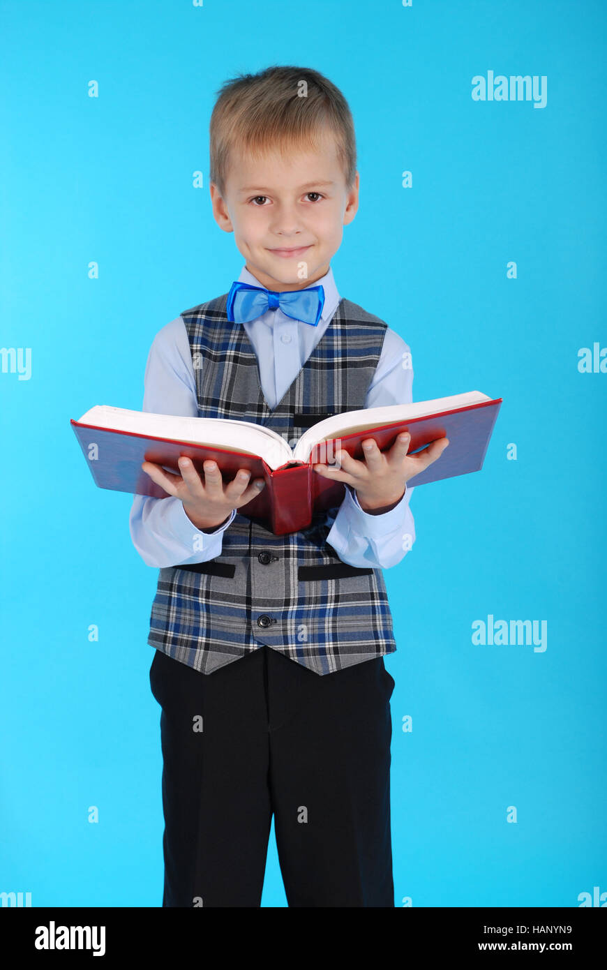 Boy in school uniform holding an open red book on a blue background ...