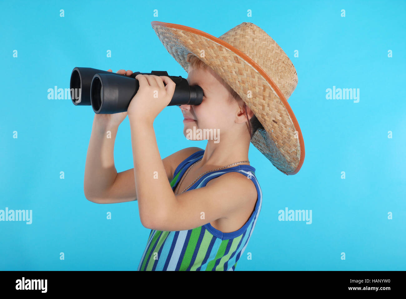 Curious boy in cowboy hat looking through binoculars. Photo on a blue ...