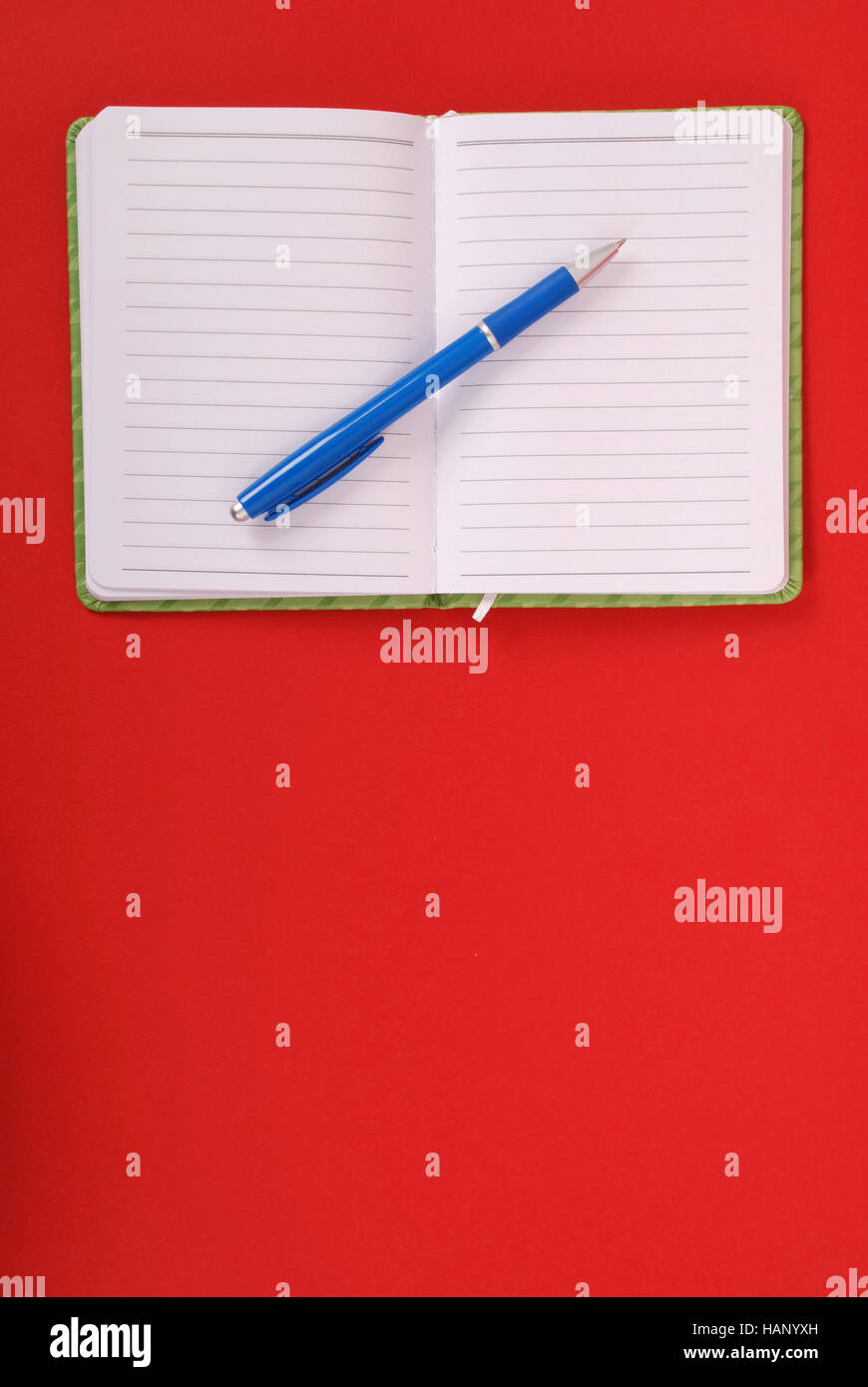 Green notebook with blue pen isolated on red background with soft ...
