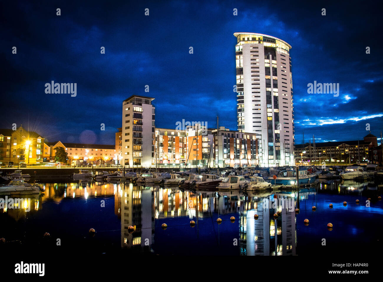 beautifully lit marina boats moored with cityscape reflecting in water ...
