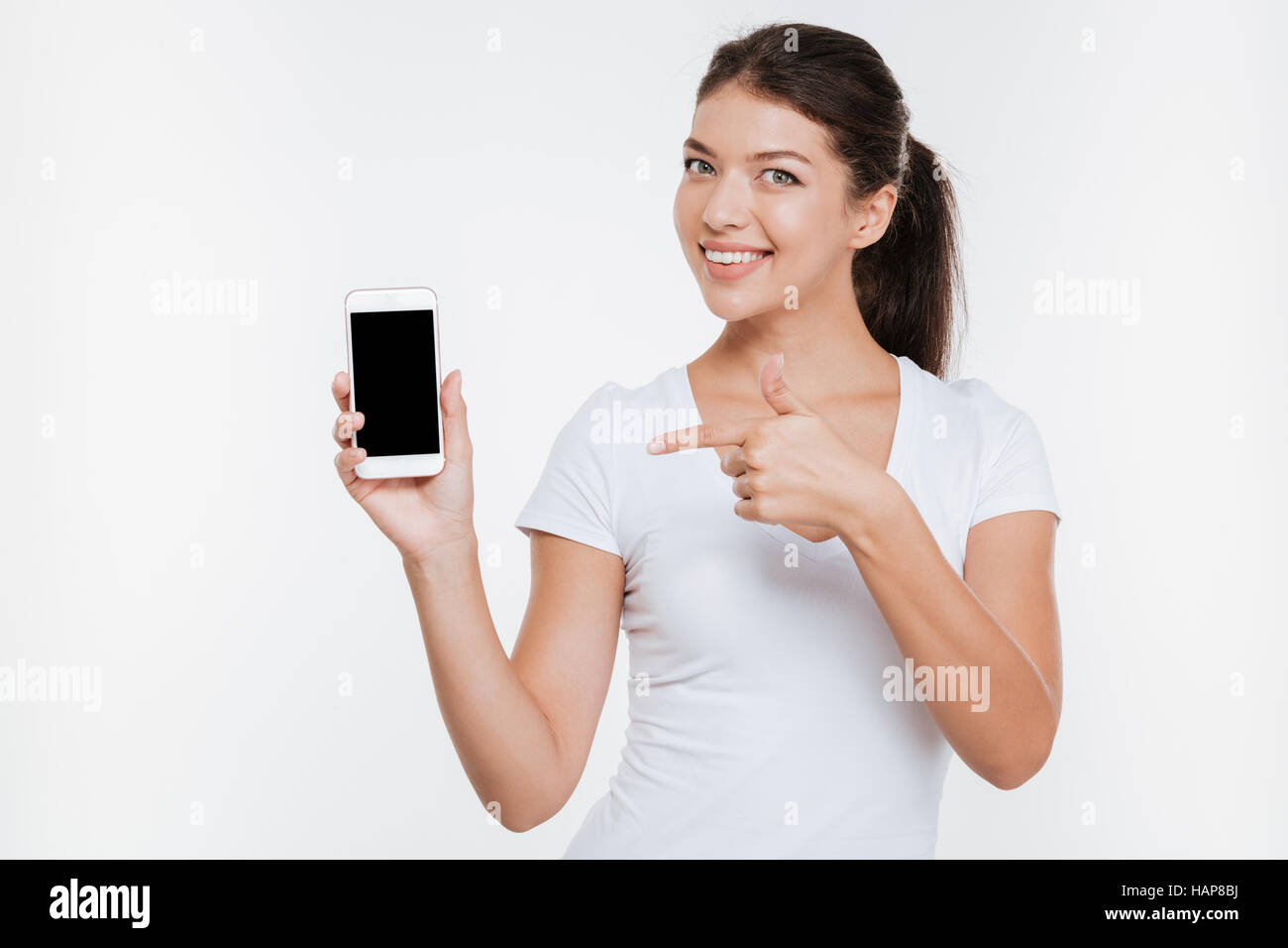 Young model in t-shirt showing at phone in studio. Isolated white ...