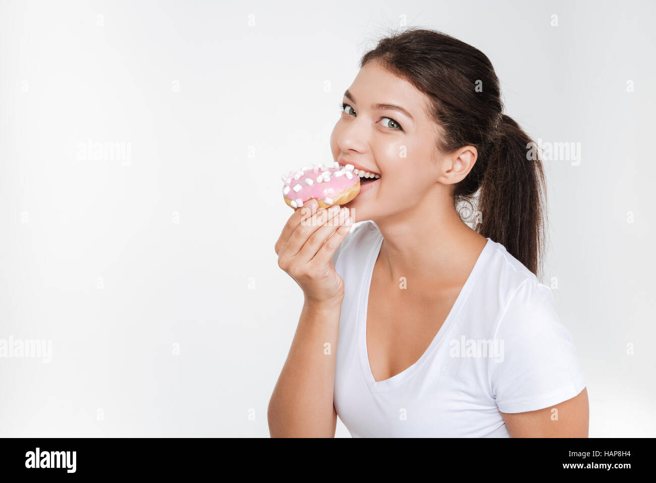 Photo of cheerful young woman eating tasty donut isolated over white ...