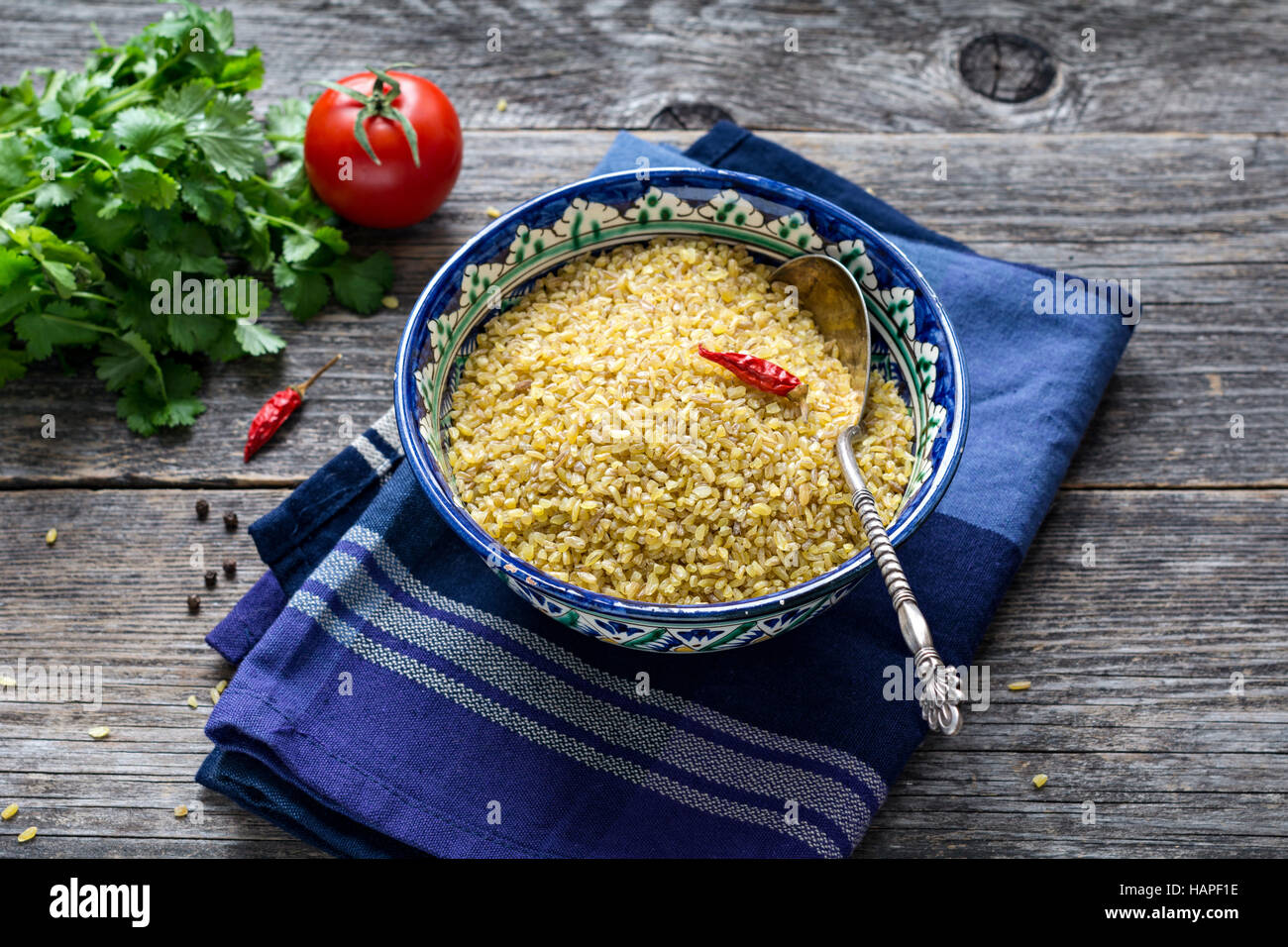 Raw bulgur wheat grains in colorful arabic bowl, fresh parsley, tomato ...