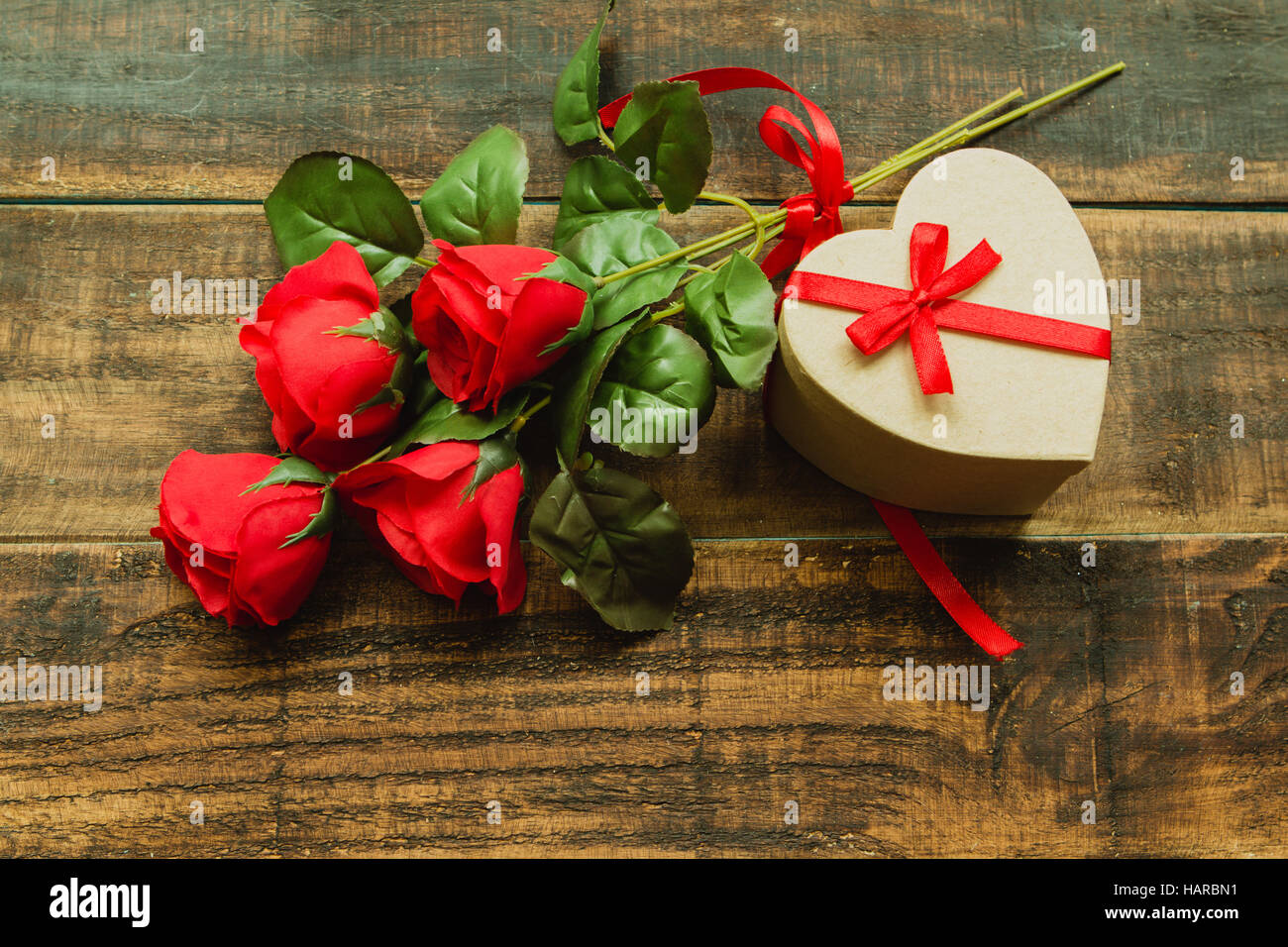 Beautiful gift with heart shape with a bouquet of red roses on a wood ...