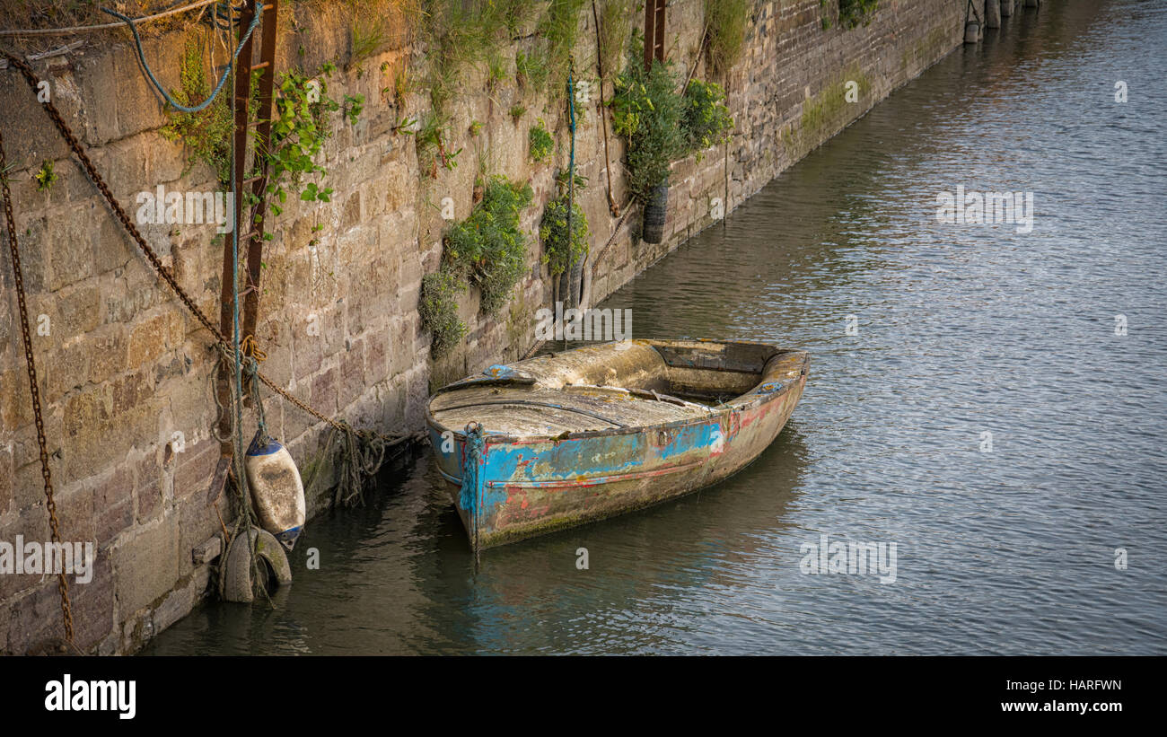 unused old wooden blue rowing boat moored up on a small river, moss ...
