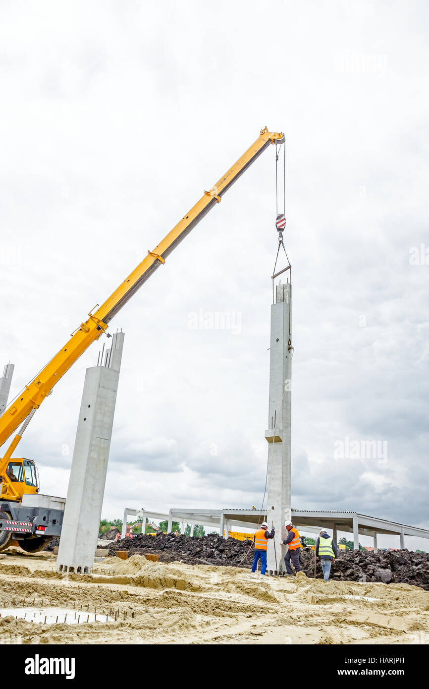 Mobile crane is operating to assembly concrete pillar on new edifice ...