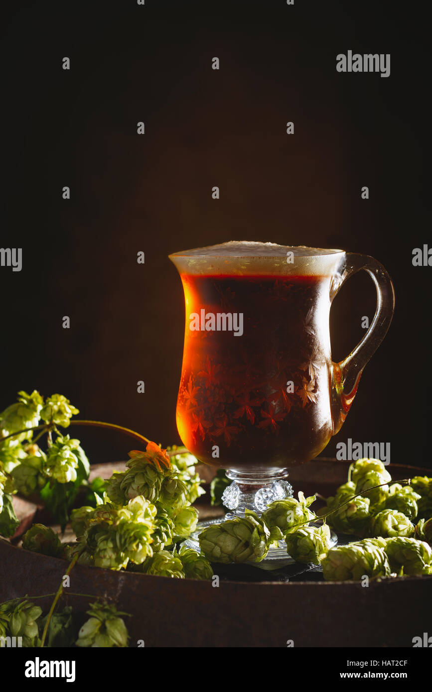 Antique glass tankard filled with ale on a rustic barrel with hops ...