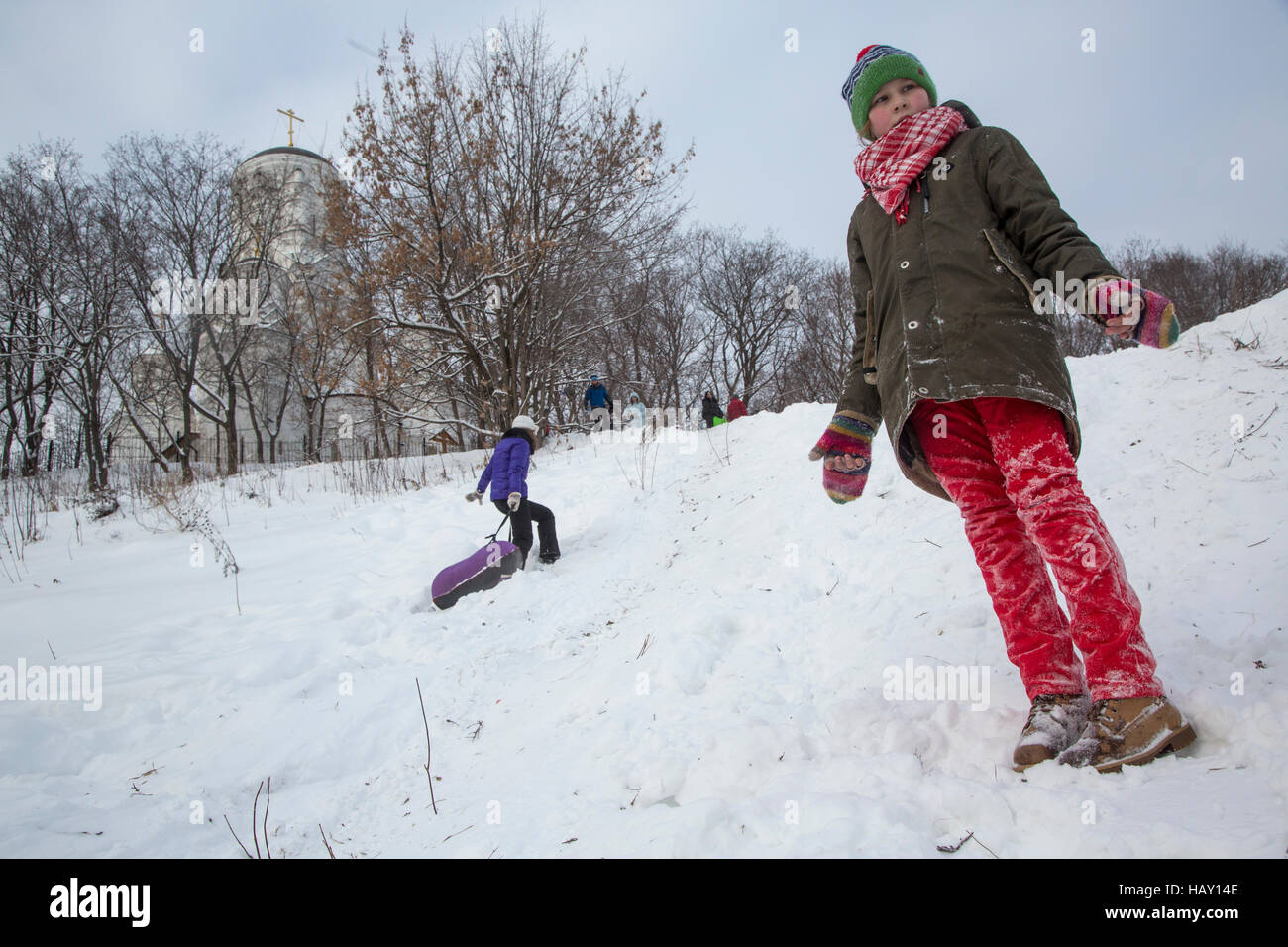 Young people riding sled down from snow slope in snowfall at Moscow ...