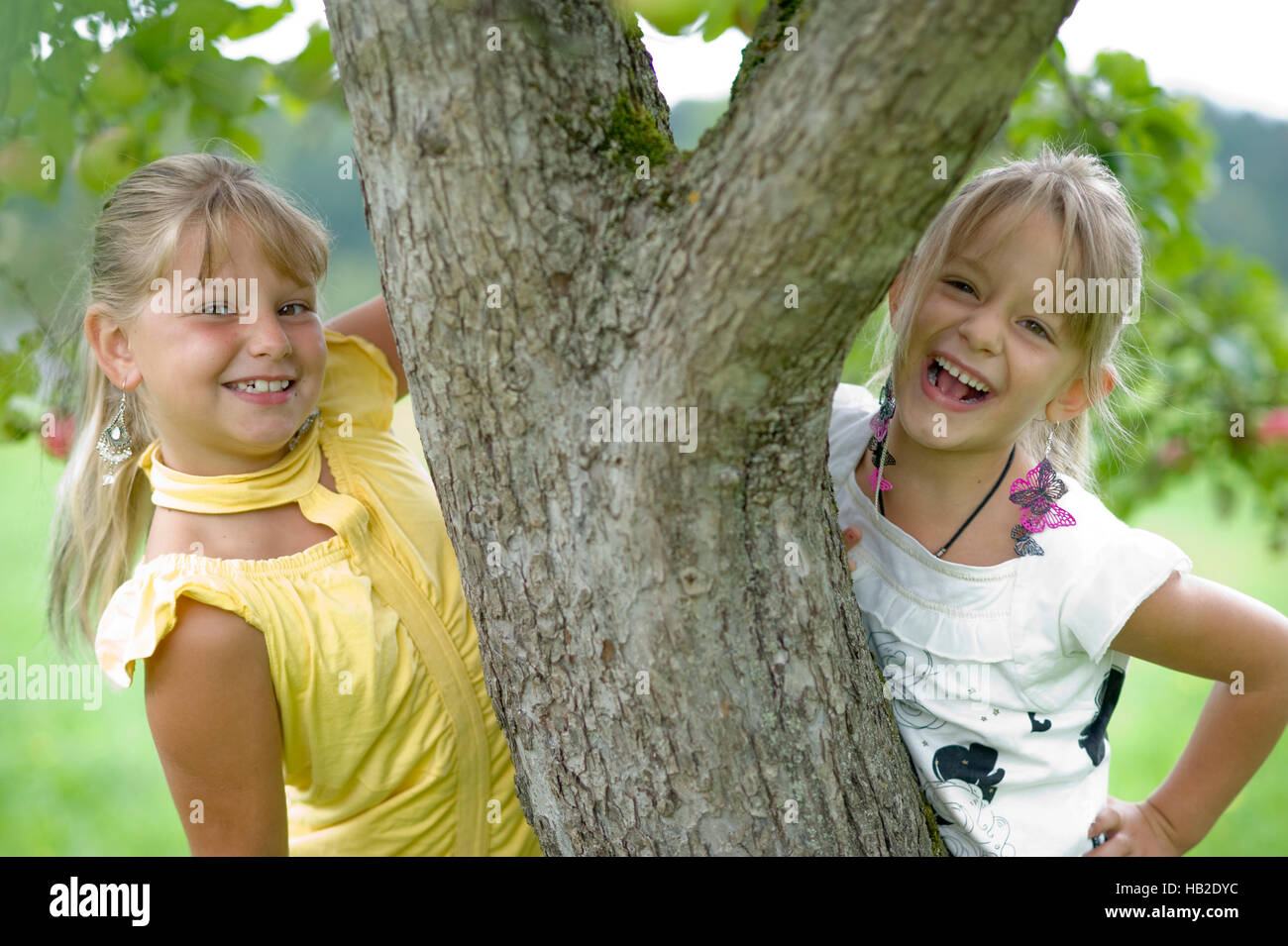 Two happy girls standing next to a tree trunk Stock Photo - Alamy
