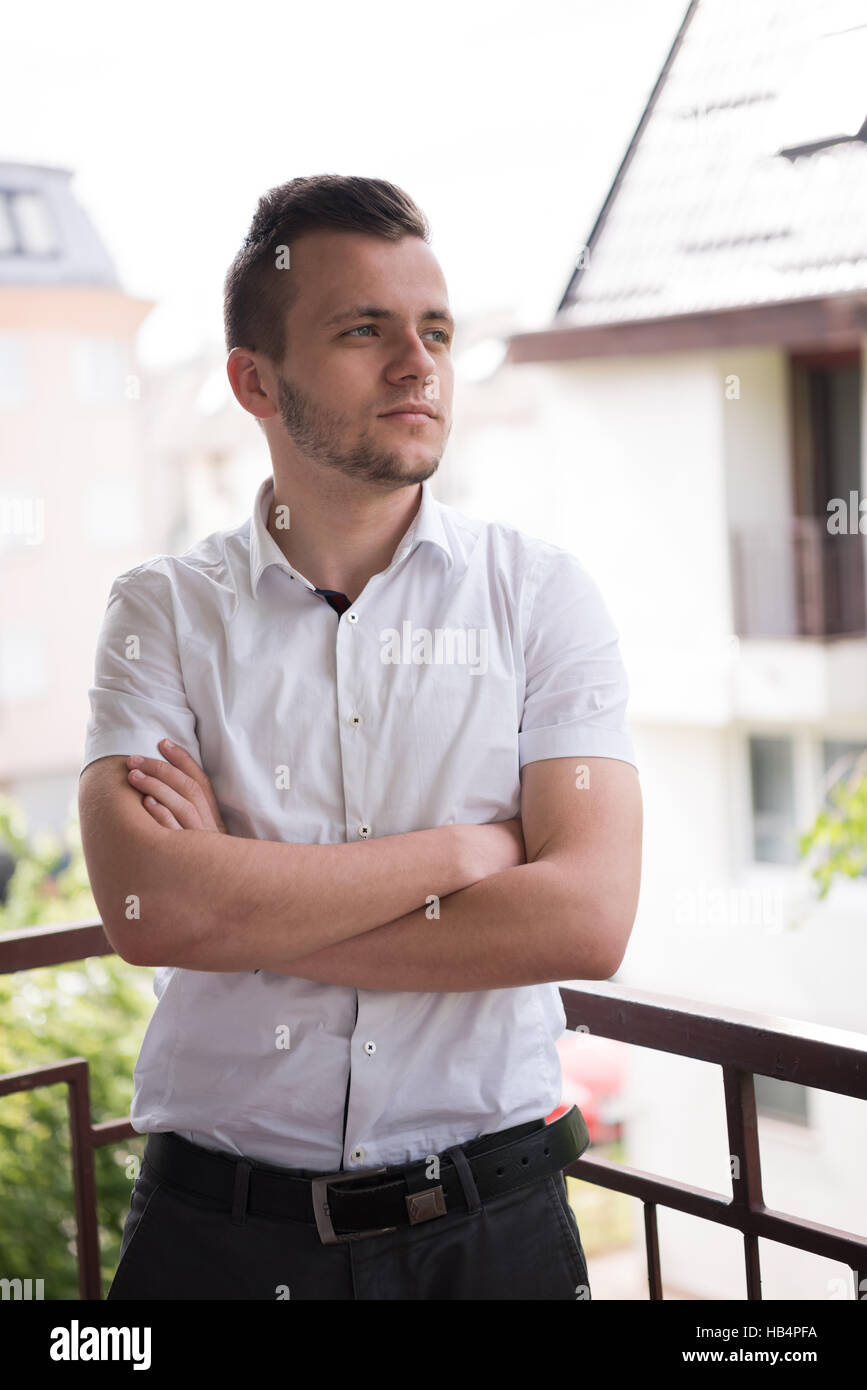 young elegant fashion man standing at balcony with arms crossed and ...