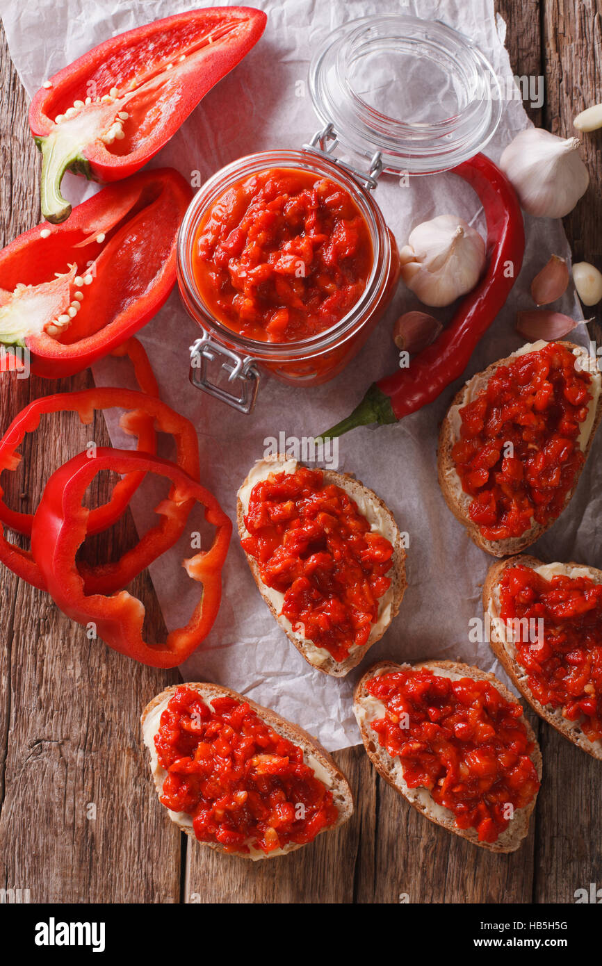 Ajvar in a glass jar and toast on a wooden background. vertical view ...