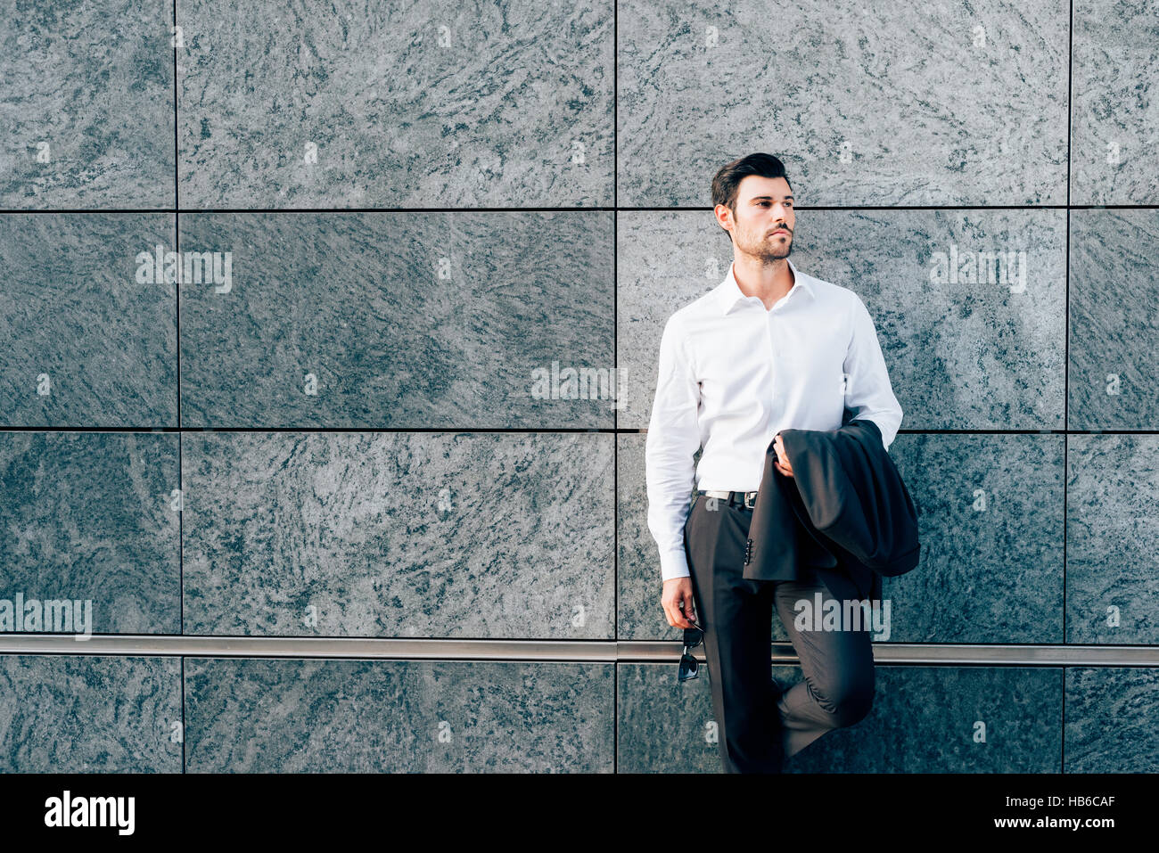 Young handsome modern businessman posing leaning against a wall ...