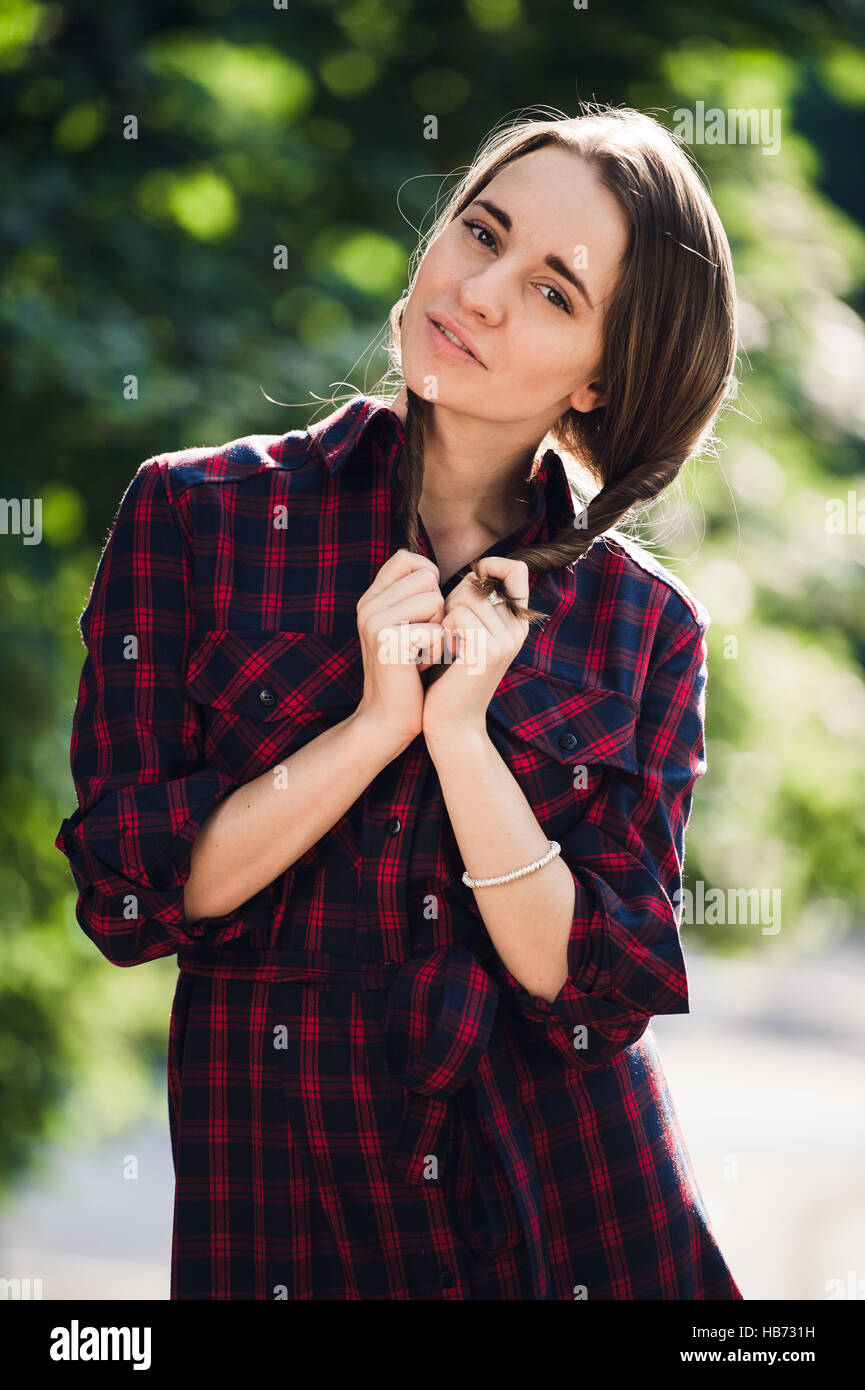 Cute teenage girl in casual dress playing with her braids, looking at camera and smiling ...