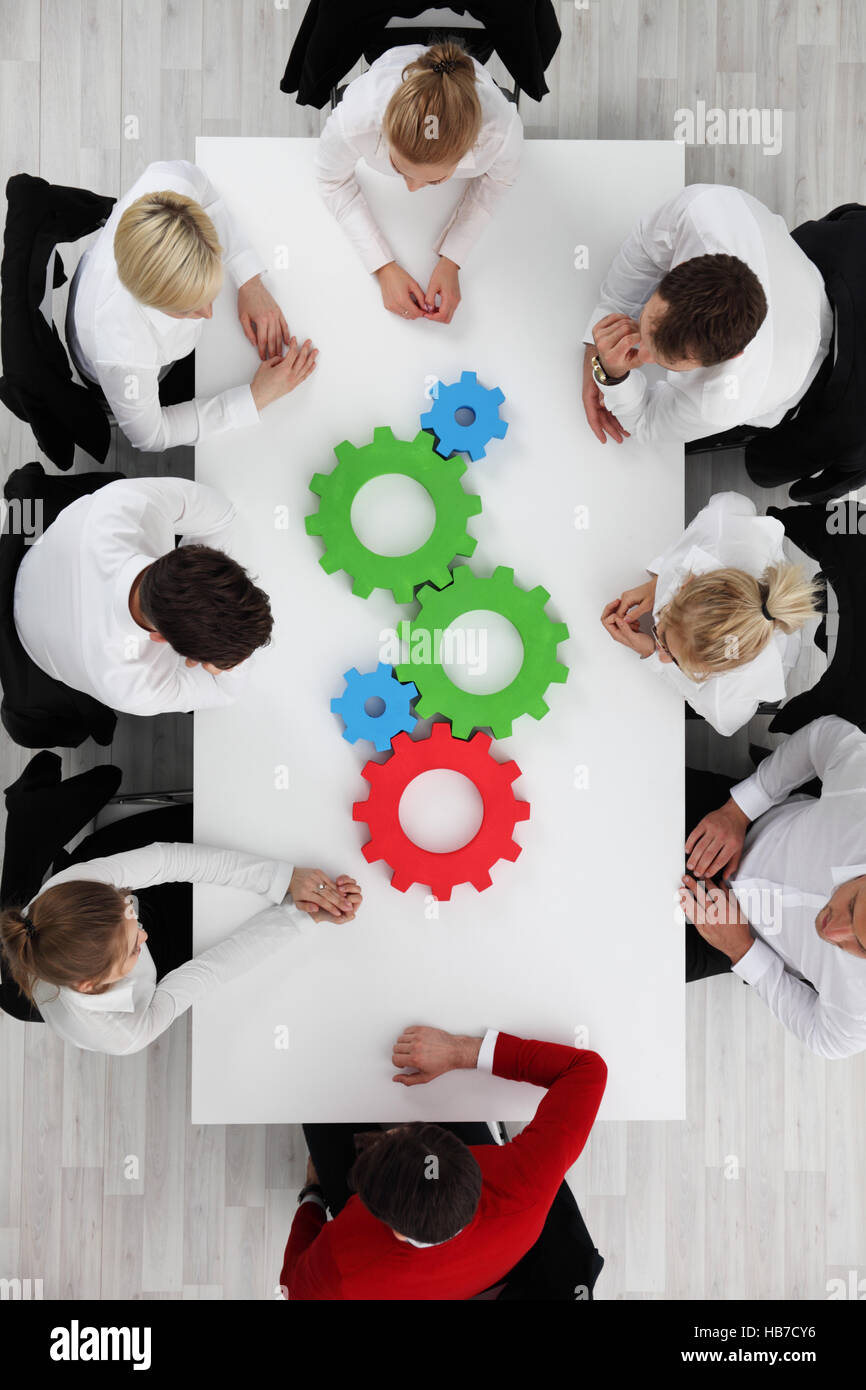 Business team sitting around the table with cogs, teamwork concept ...