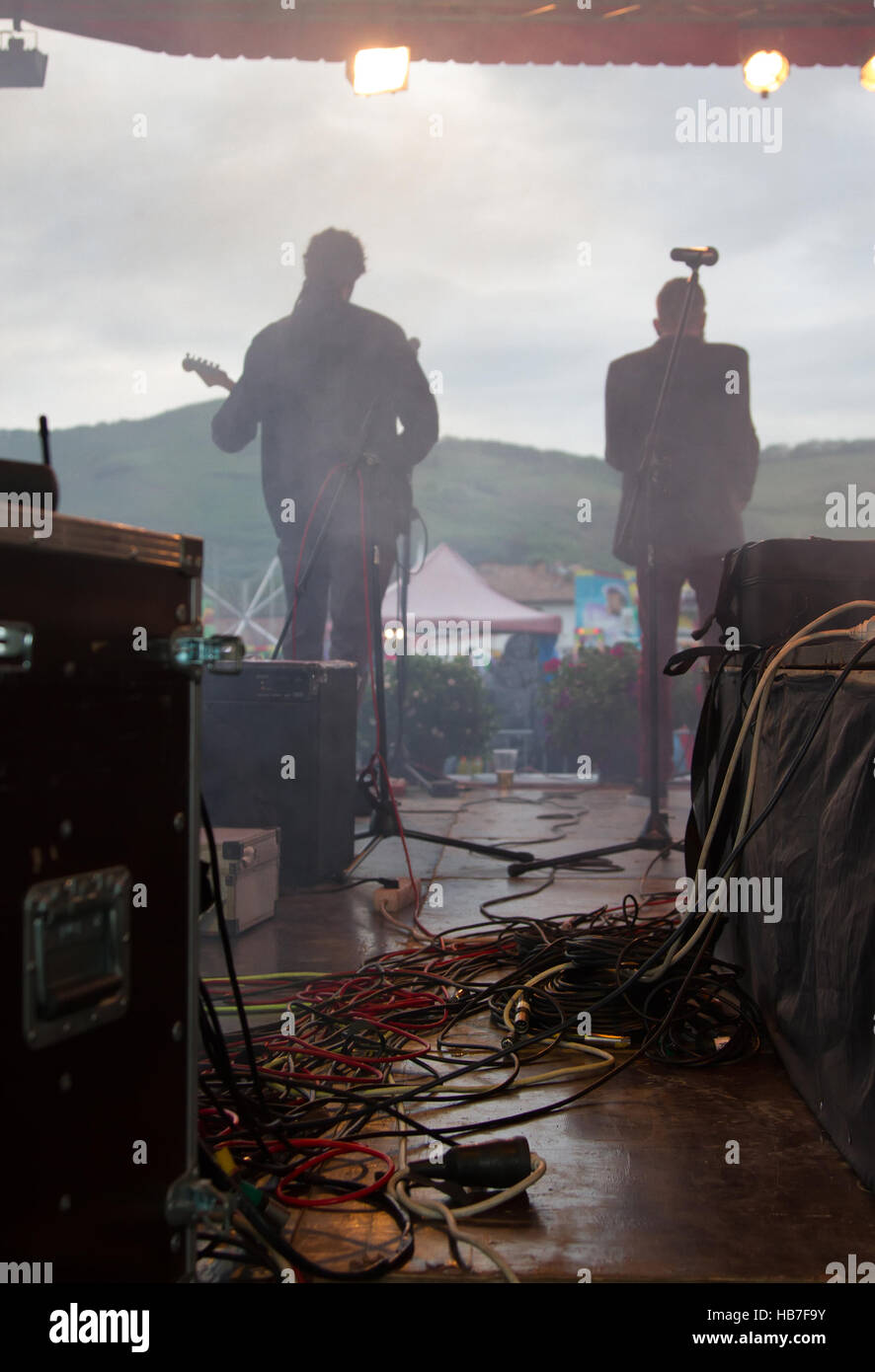backstage of an outdoor concert with two perfomers and lots of cables ...