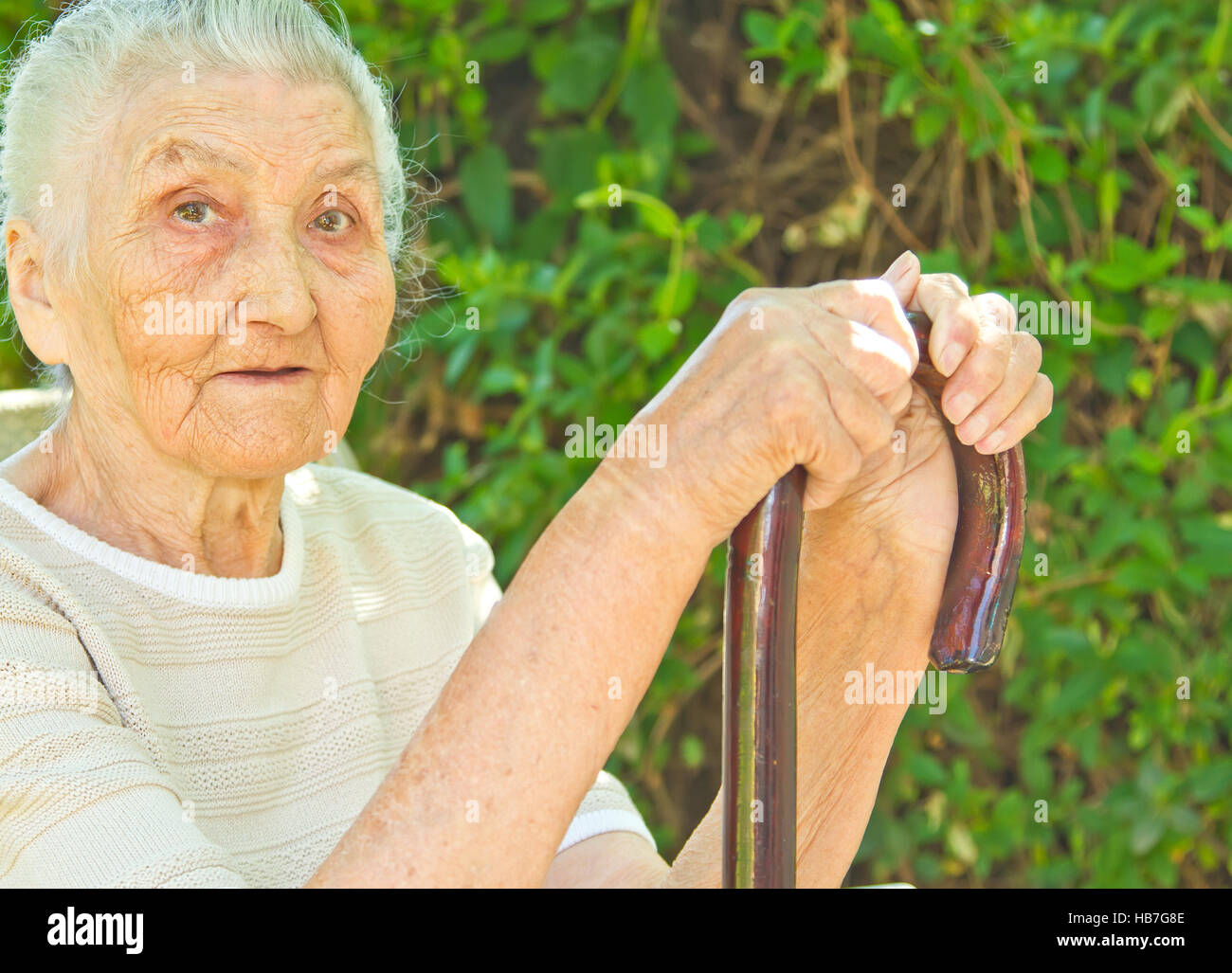 very old woman sitting in the park and standing against a walking stick Stock Photo - Alamy