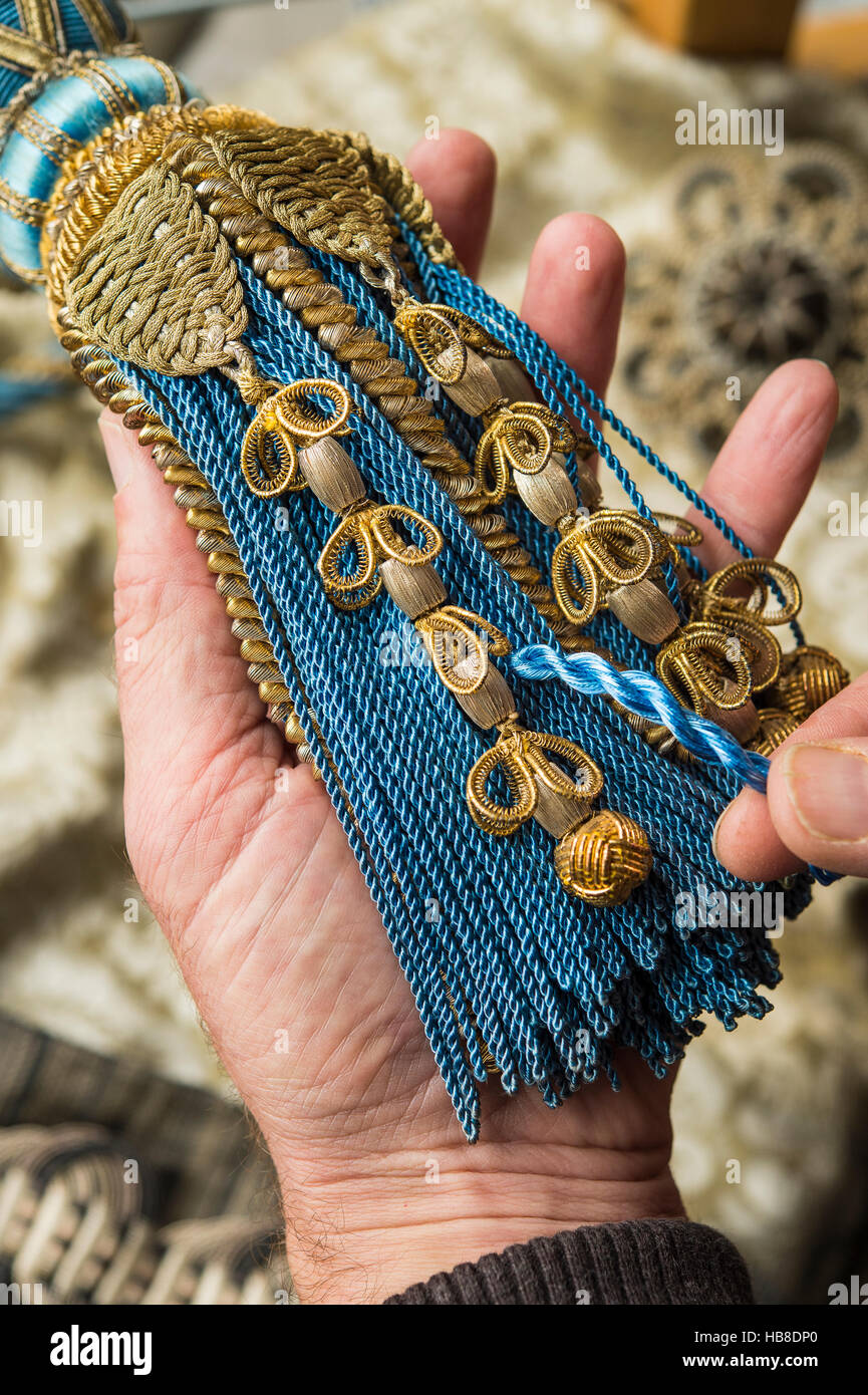 Passementerie maker, hand holding blue and gold cord tassel and ...