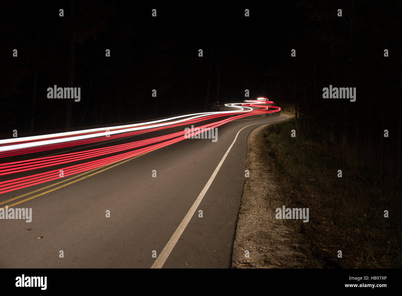 Curved road at night with cars driving up and down causing light trails ...