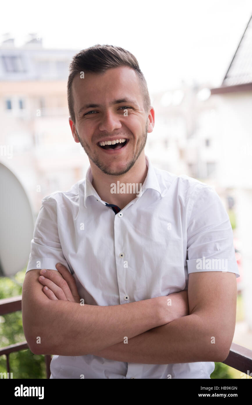young elegant fashion man standing at balcony with arms crossed and ...