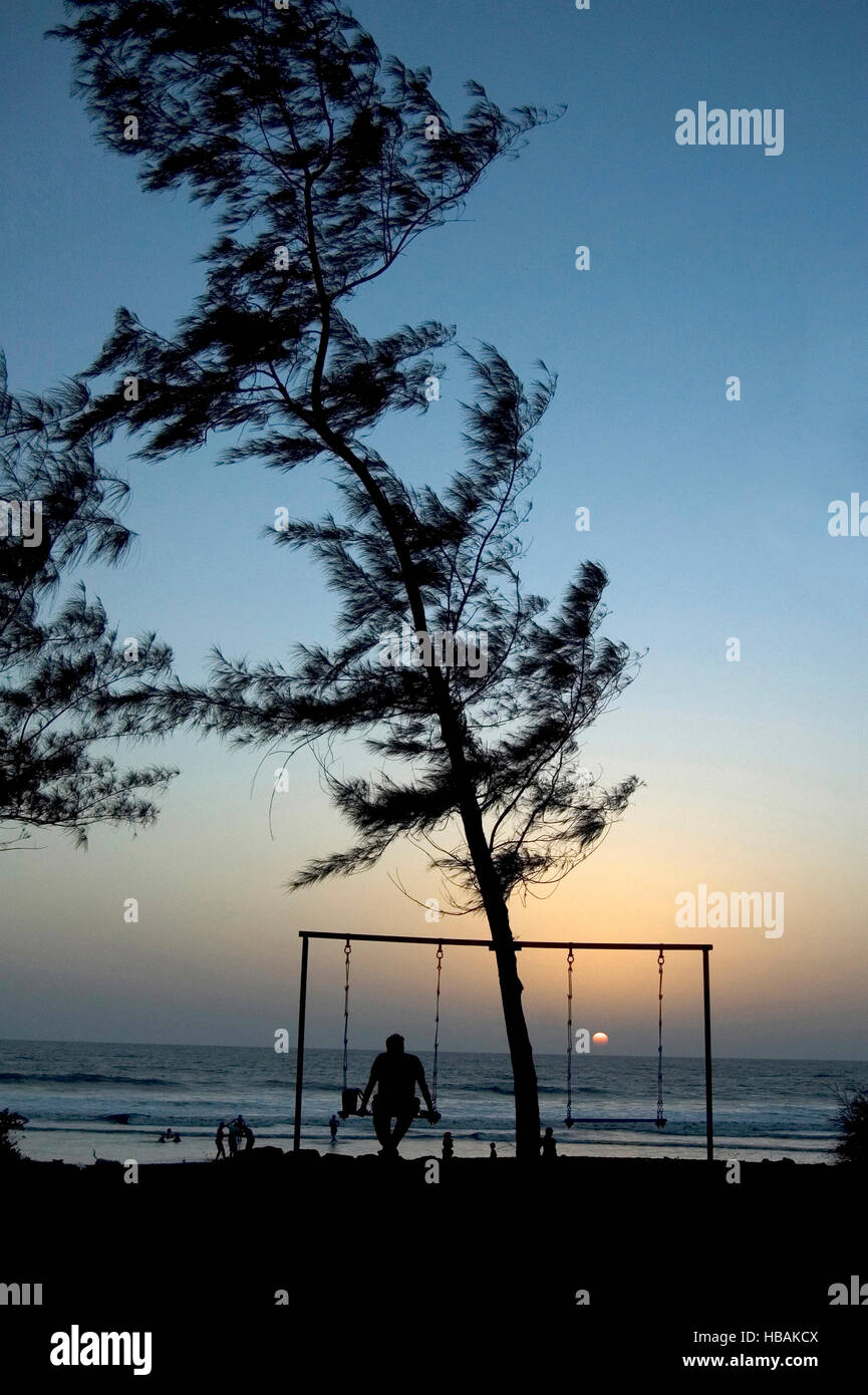 Silhouette of man sitting with sunset in background. Shiroda beach ...